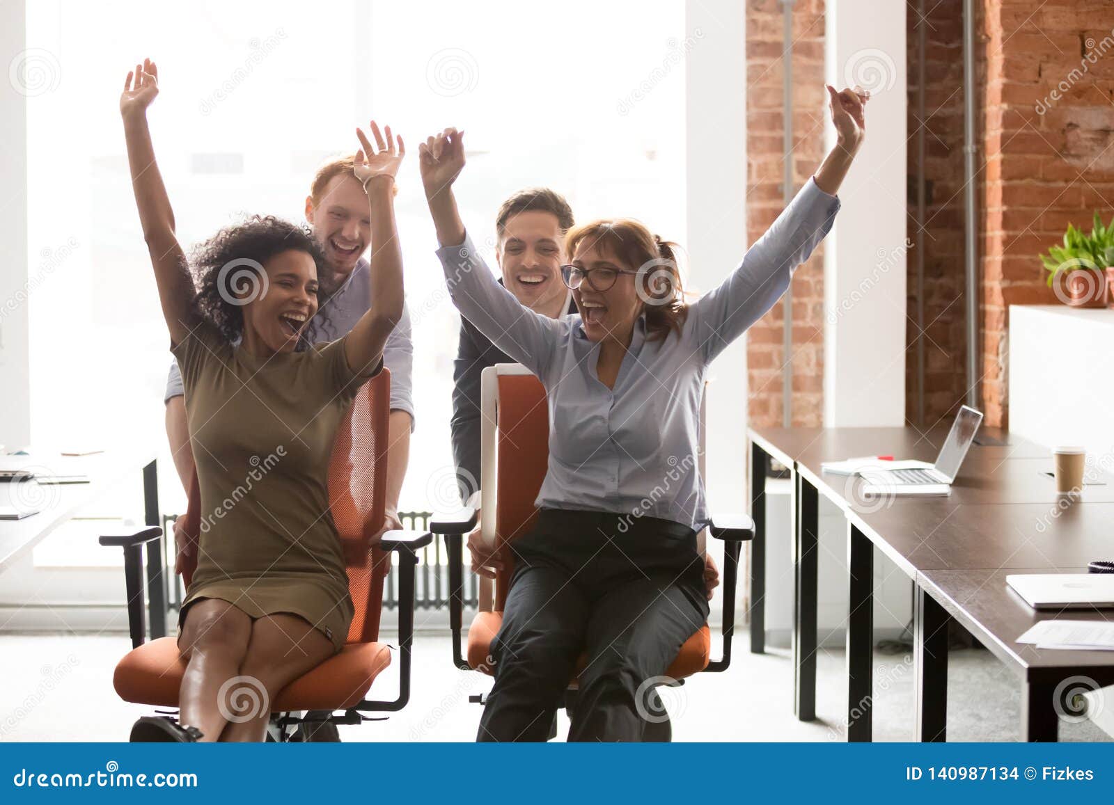 Happy Multicultural Office Workers Laughing Having Fun Riding on Chairs ...