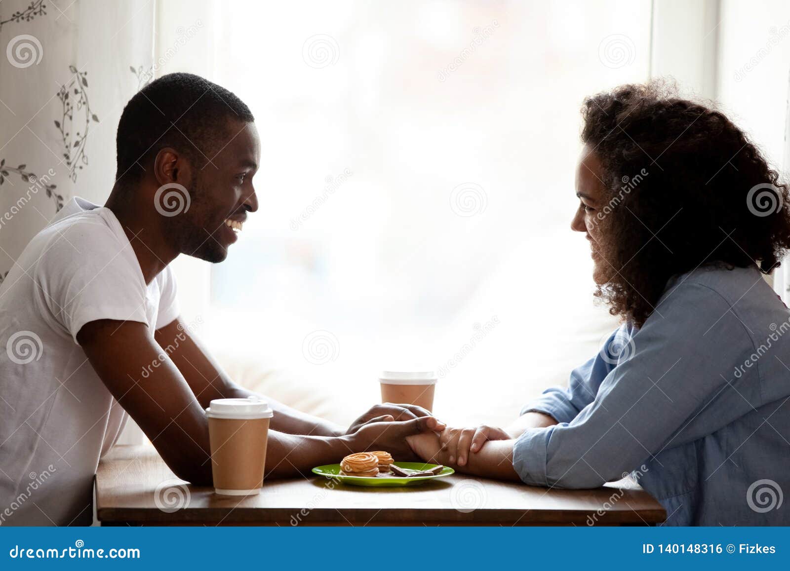 Happy Multiracial Couple Holding Hands Enjoying Date In Cafe Stock