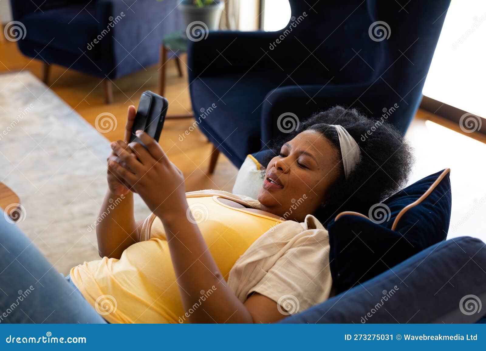 Happy Plus Size African American Woman Lying On Sofa And Using