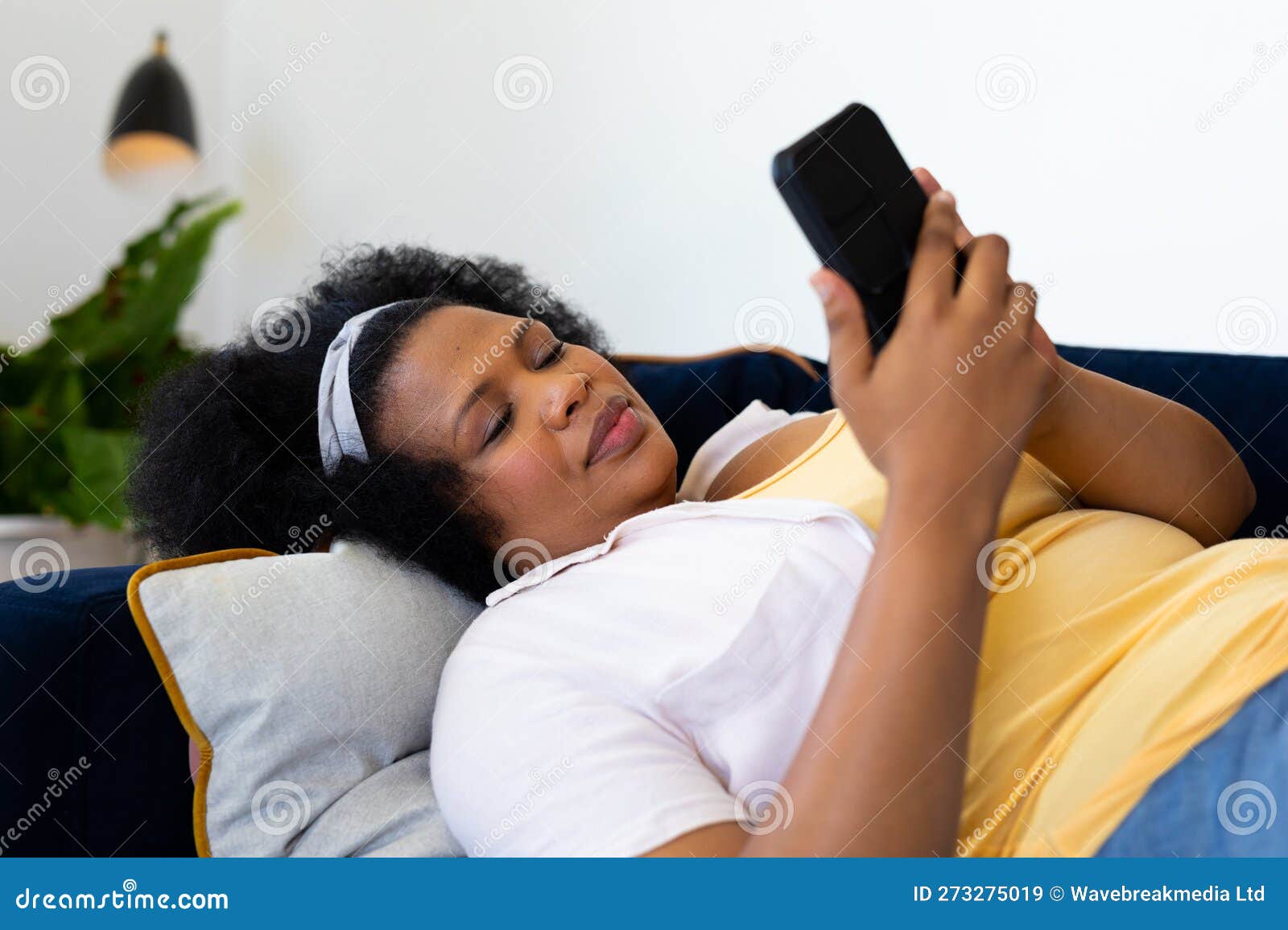 Happy Plus Size African American Woman Lying On Sofa And Using