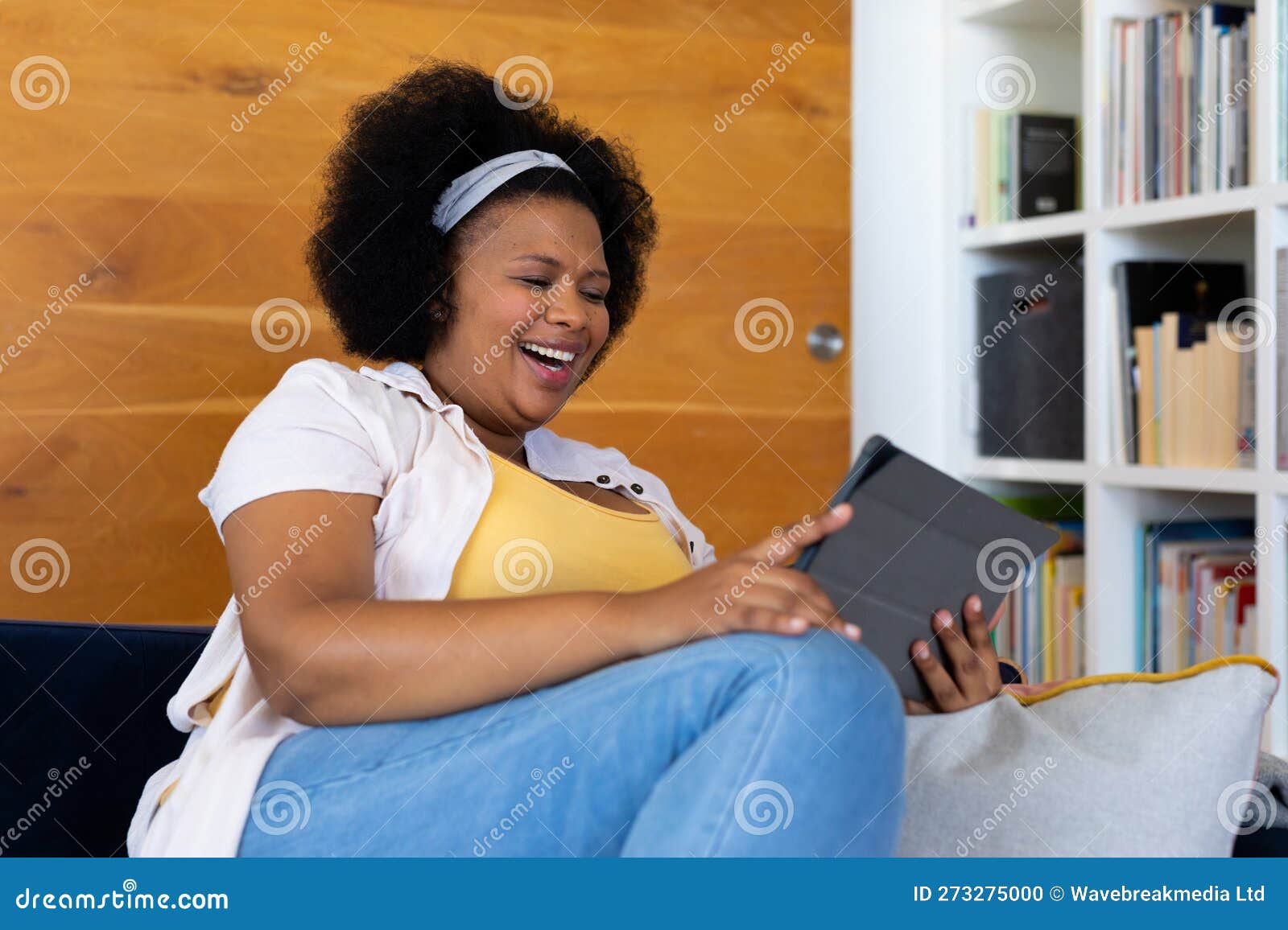 Happy Plus Size African American Woman Sitting On Sofa And Using Tablet