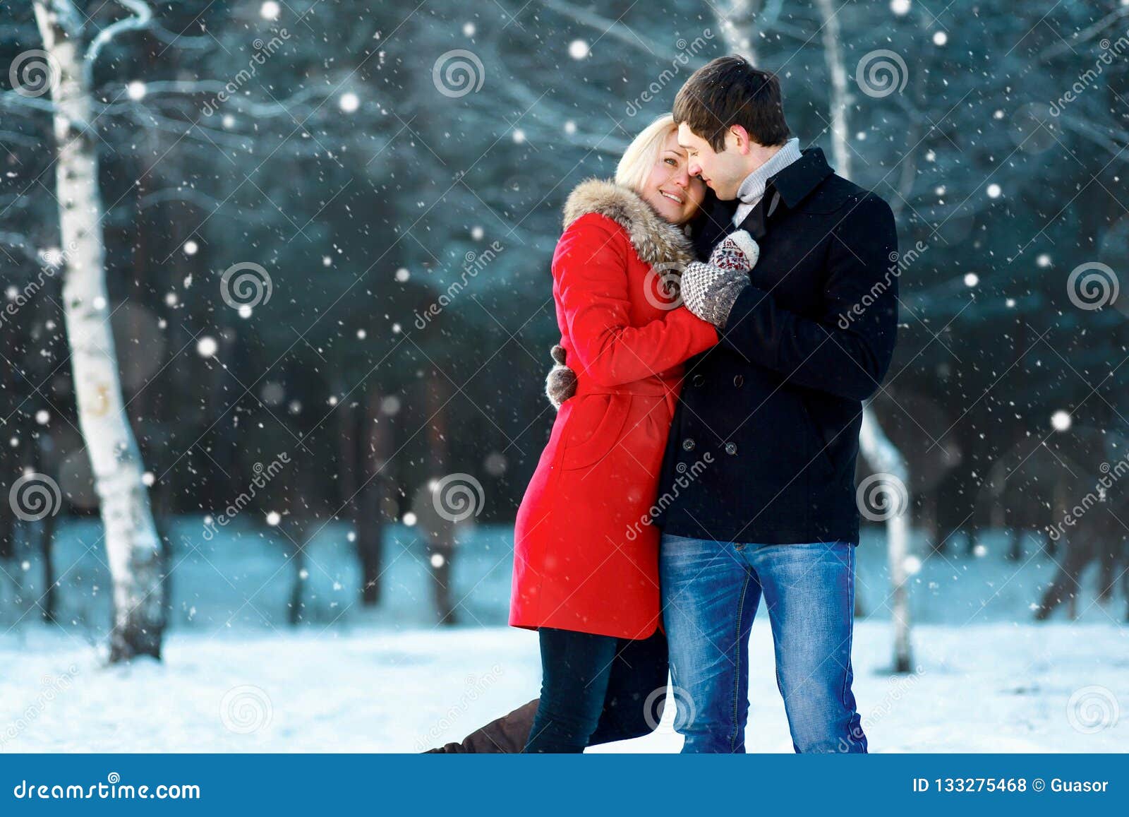 Happy Romantic Young Couple Walking In Winter Park On Flying Snowflakes