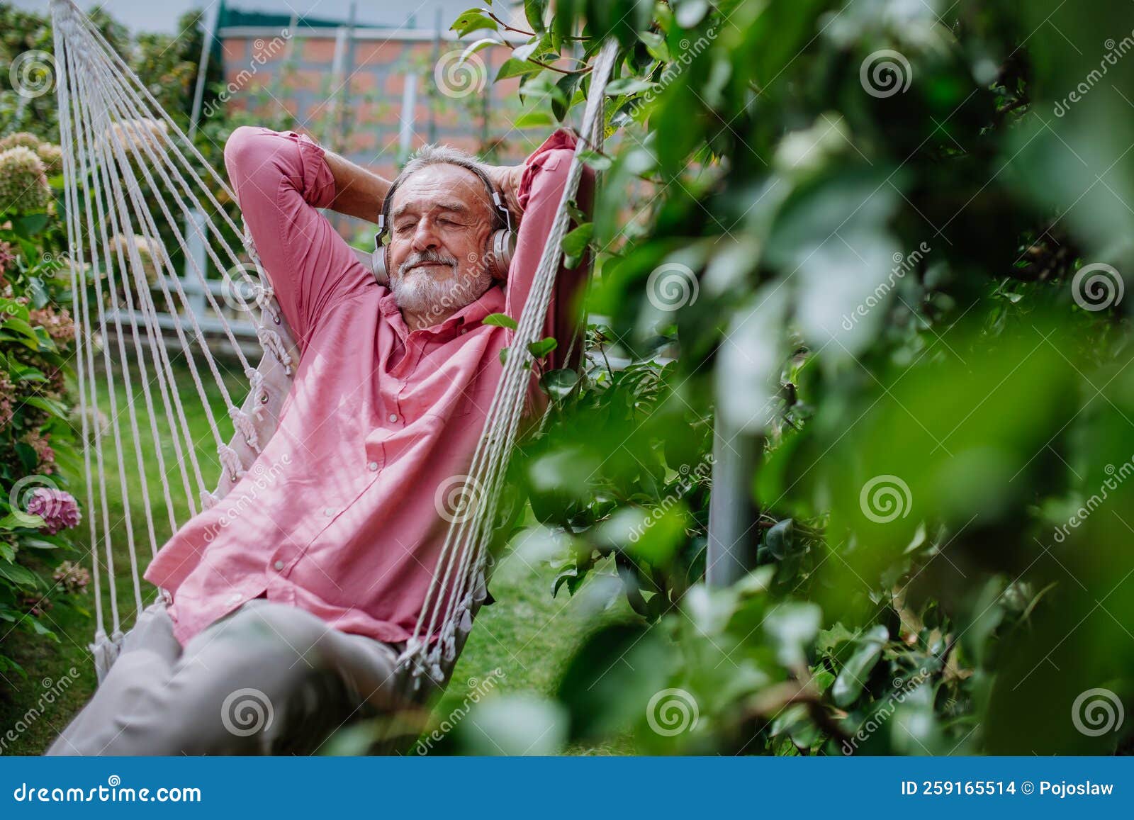 Happy Senior Man Relaxing And Listening Music In Outdoor Swing In His