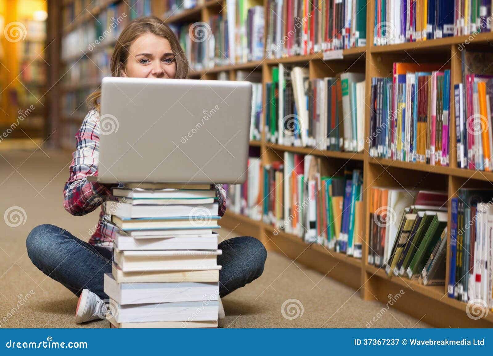Happy Student Sitting on Library Floor Using Laptop on Pile of Books ...