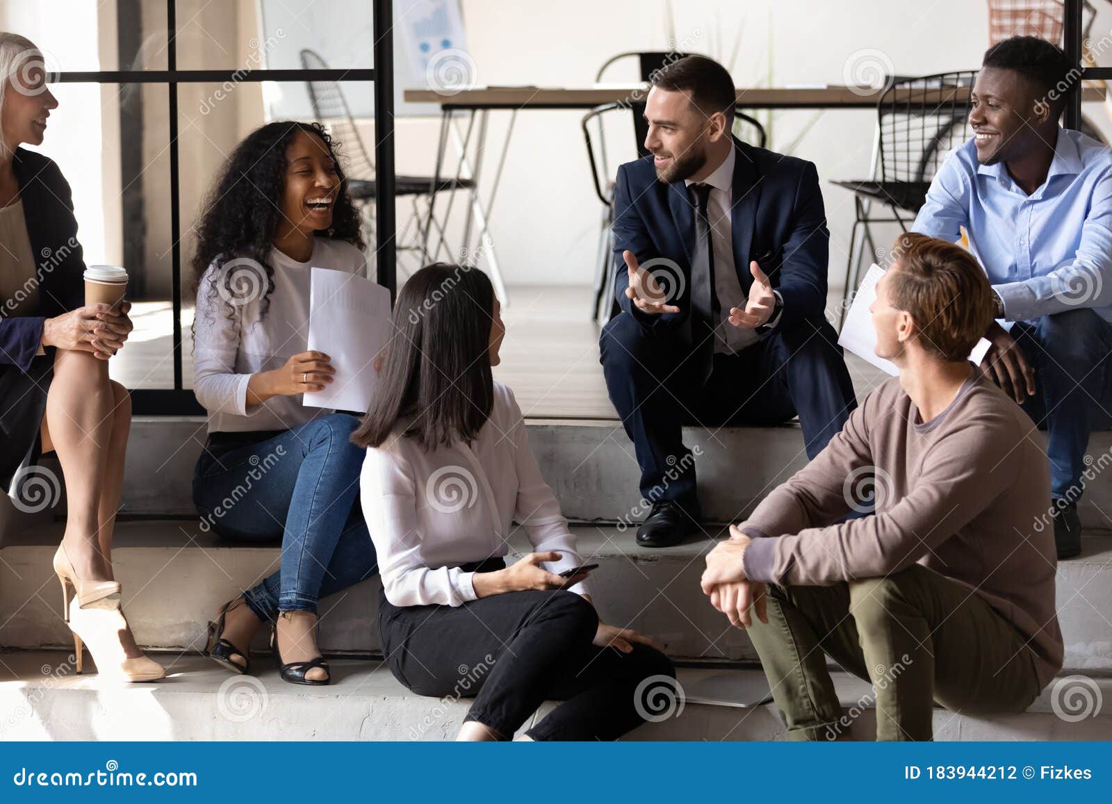 Happy Diverse Coworkers Sitting On Stairs In Office Having Fun Stock