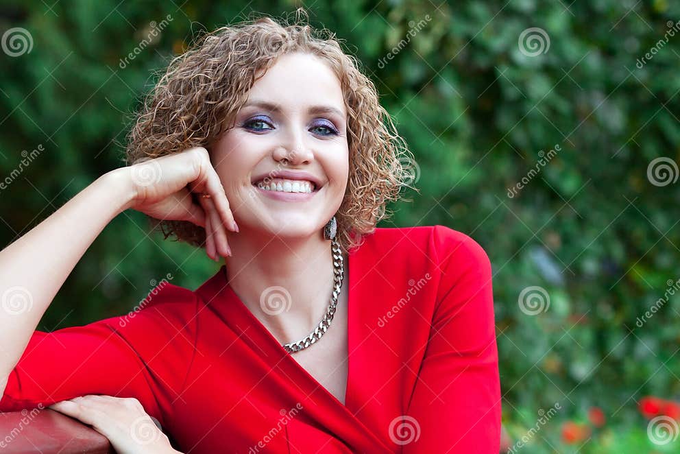 Happy Woman In Red Dress Is Sitting On A Bench In A Park And Smiling To You Stock Image Image