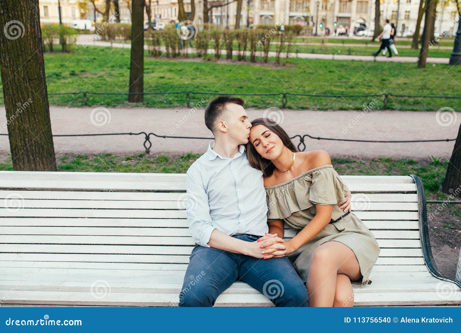 Happy Young Couple In Love Sitting On A Park Bench And Hugging Stock