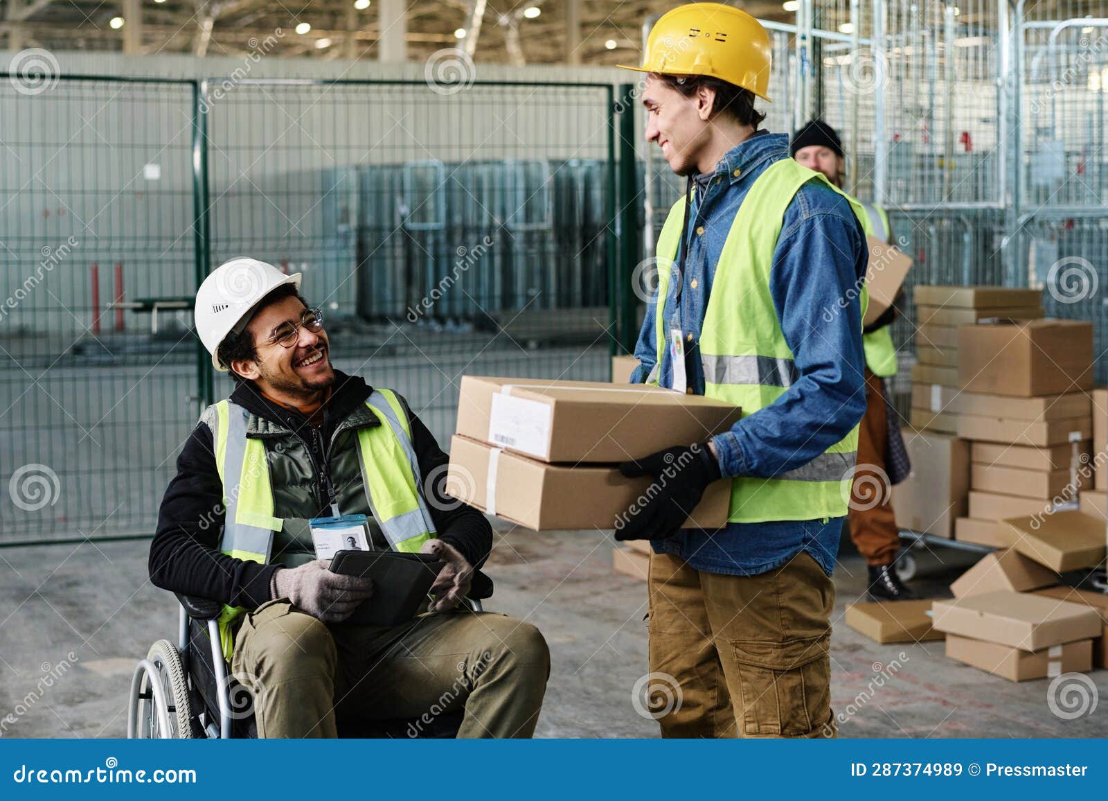 Happy Young Engineer in Wheelchair Looking at Colleague Carrying Boxes ...