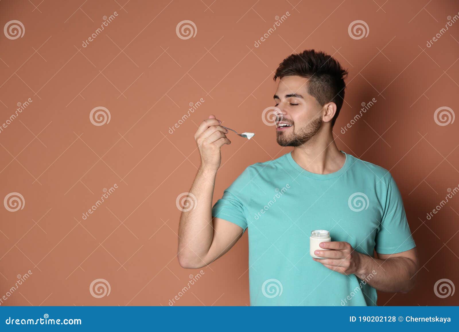 Happy Young Man Eating Tasty Yogurt on Background. Space for Text Stock ...