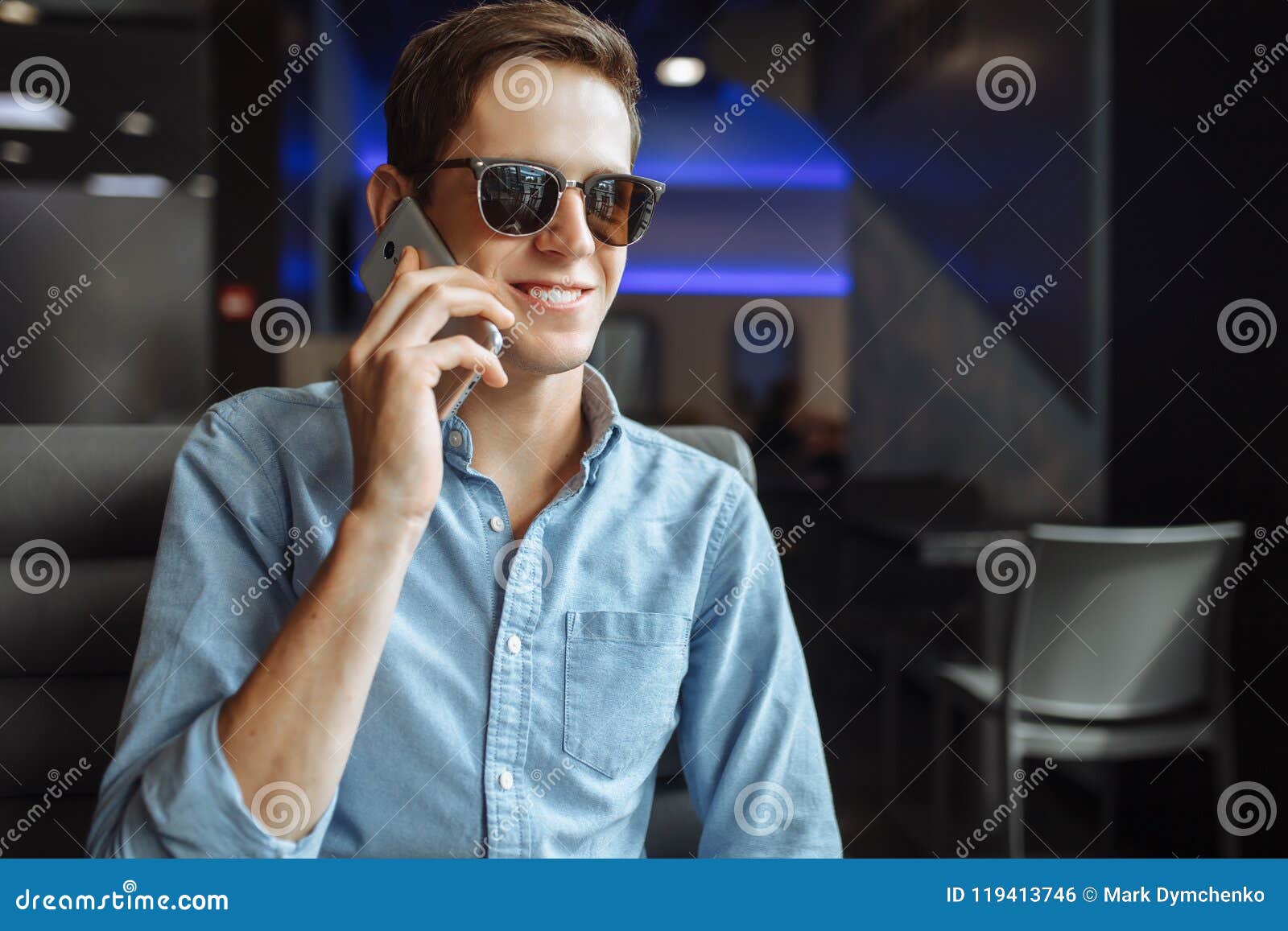 Happy Young Man In Glasses Emotionally Talking On The Phone Sitting