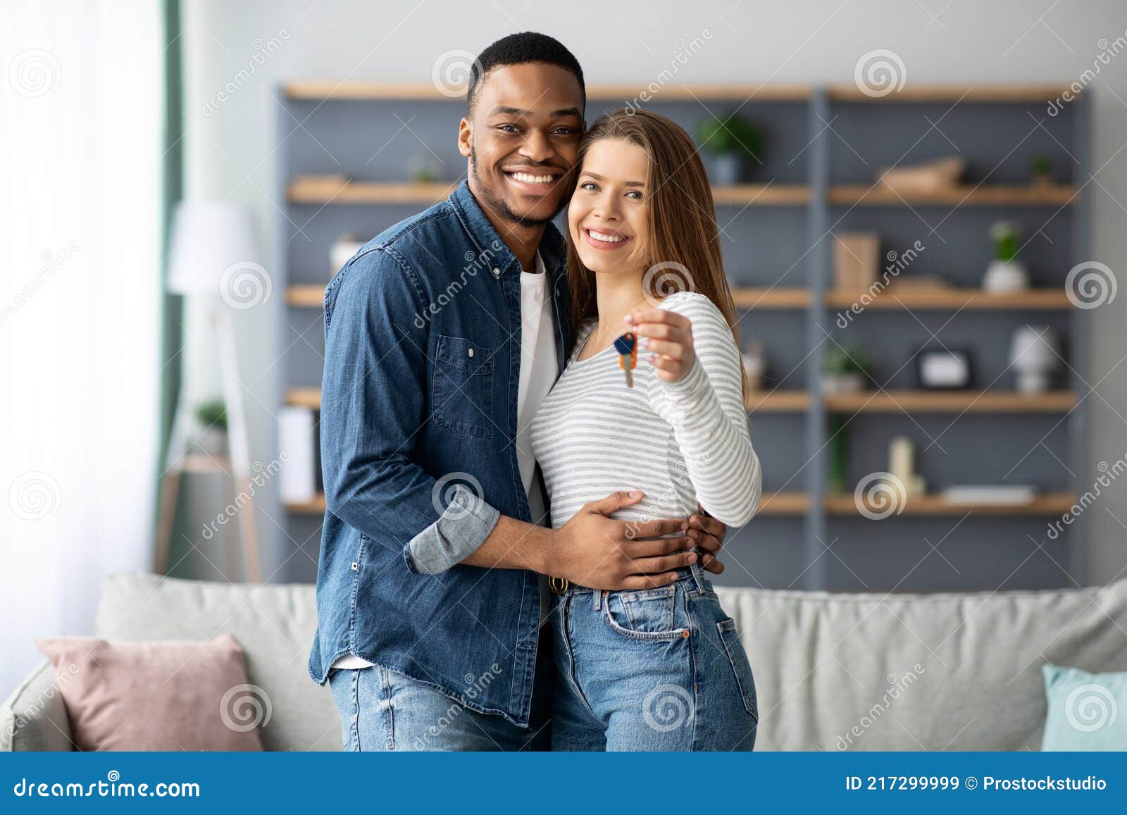Happy Young Multiracial Couple Holding Home Keys And Hugging Stock