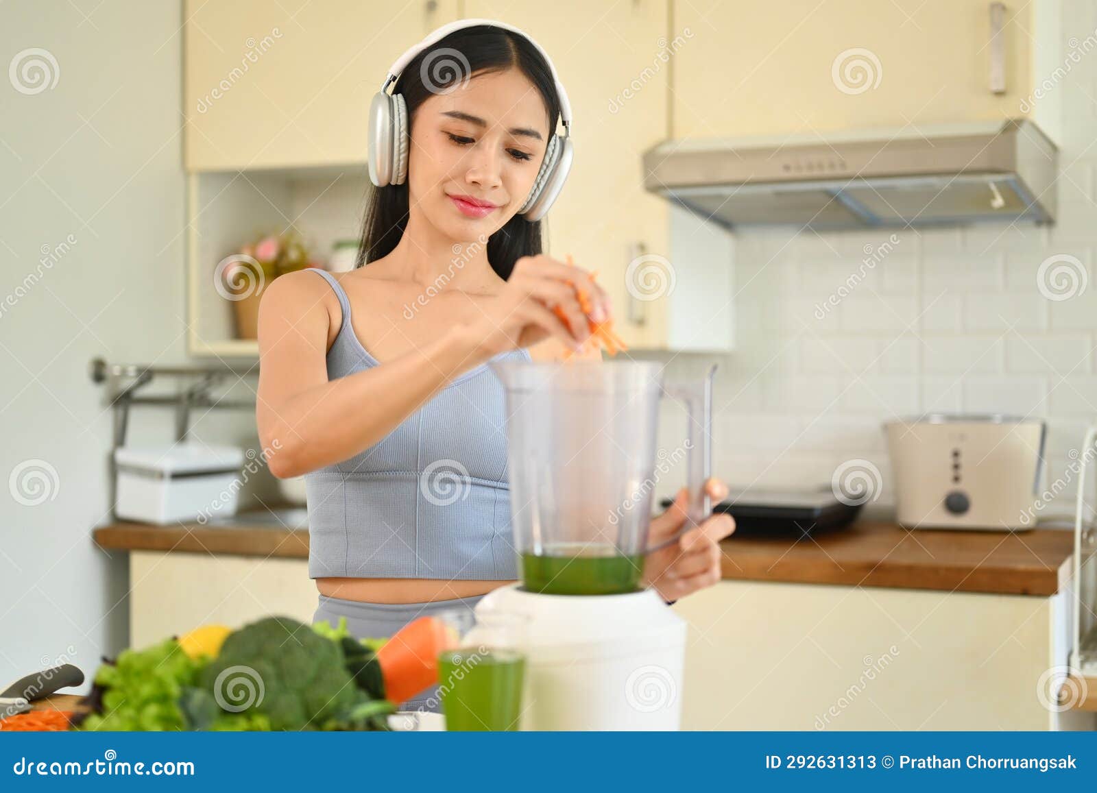 Happy Young Woman Making Healthy Green Smoothie With Blender In Kitchen