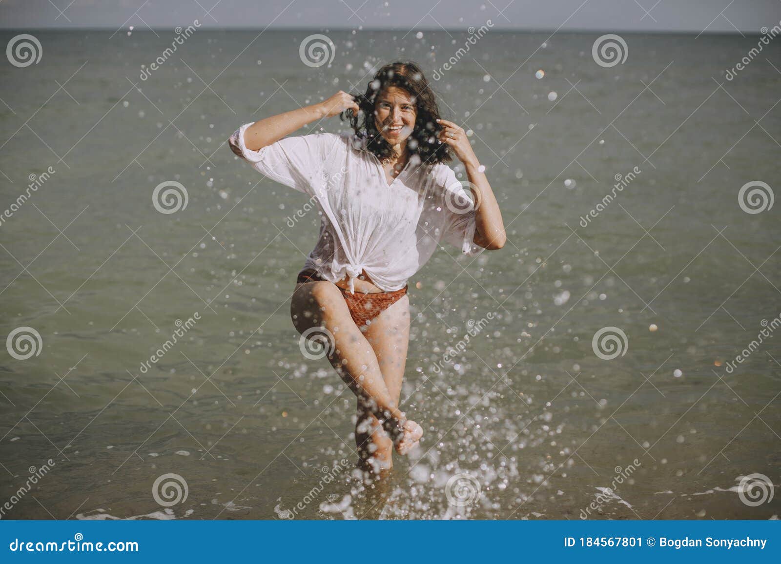 Happy Young Woman In Wet White Shirt Splashing Water Drops With Leg In