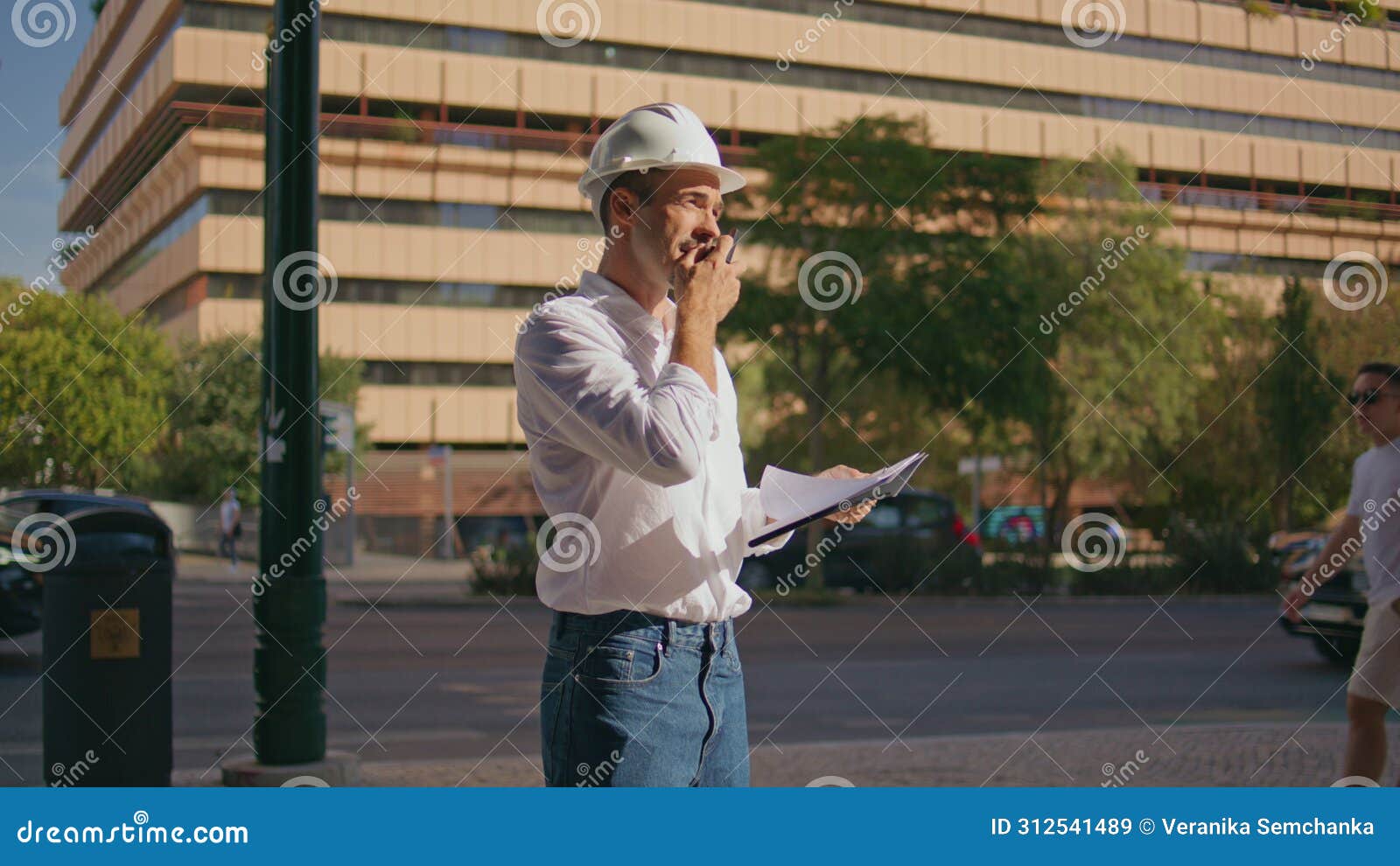 Hardhat Man Using Walkie-talkie Giving Instructions To Workers in ... Hardhat Man Using Walkie-talkie Giving Instructions To Workers in ...