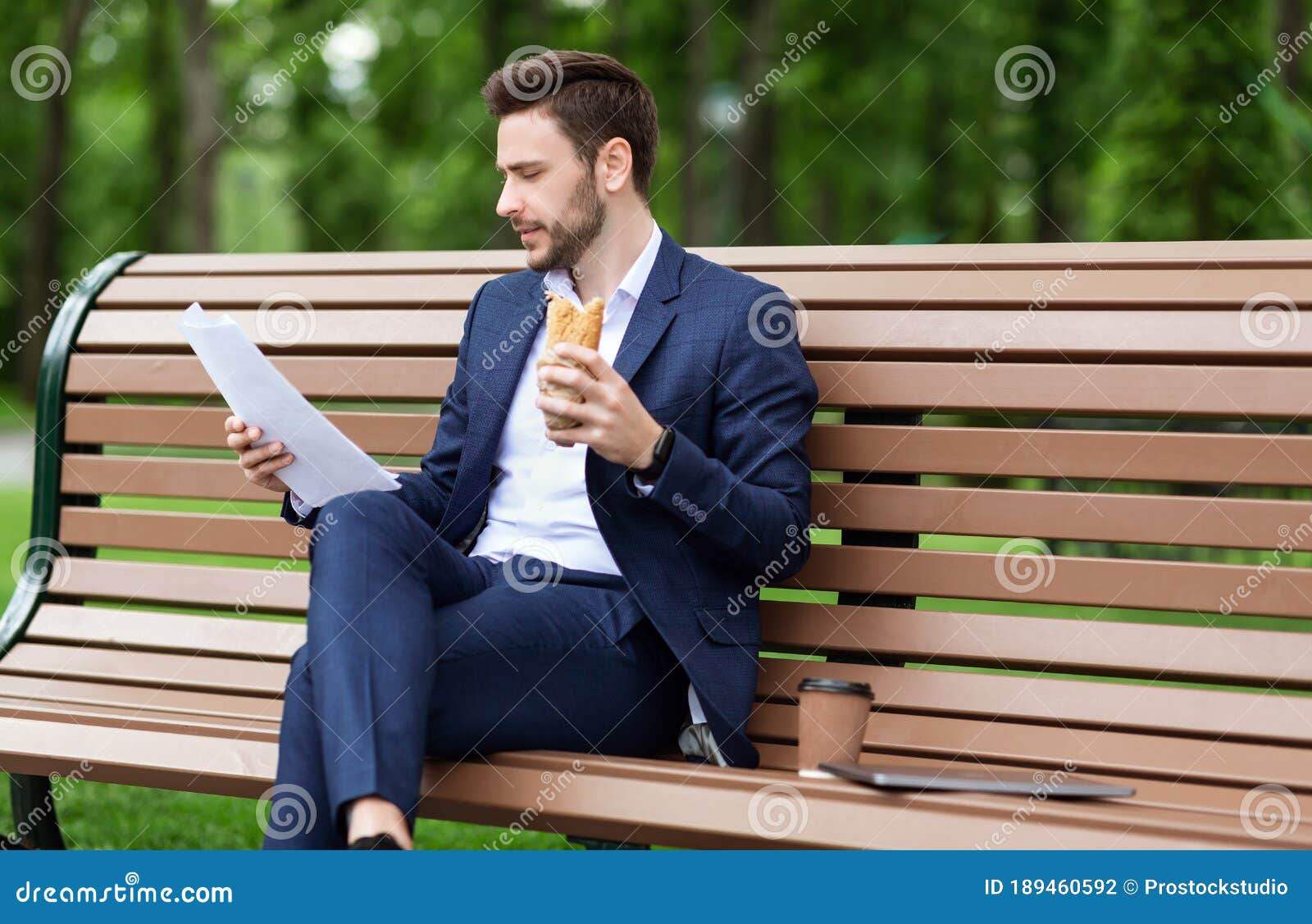 Hardworking CEO Looking through Documents while Having Lunch on Bench ...