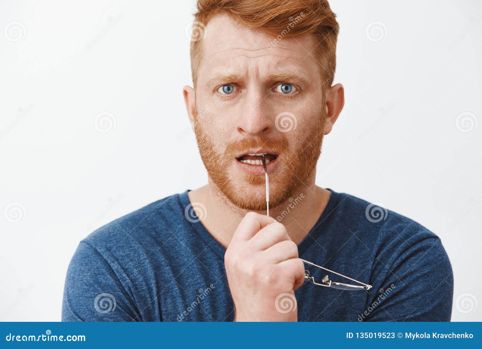 Headshot Of Worried Redhead Man With Bristle Biting Rim Of Glasses And