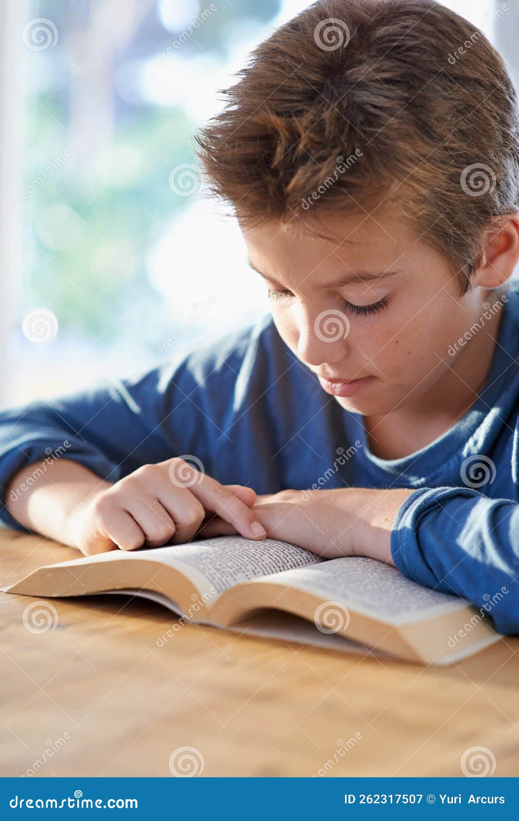Hes really Getting into it. a Young Boy Reading a Book at a Table ...