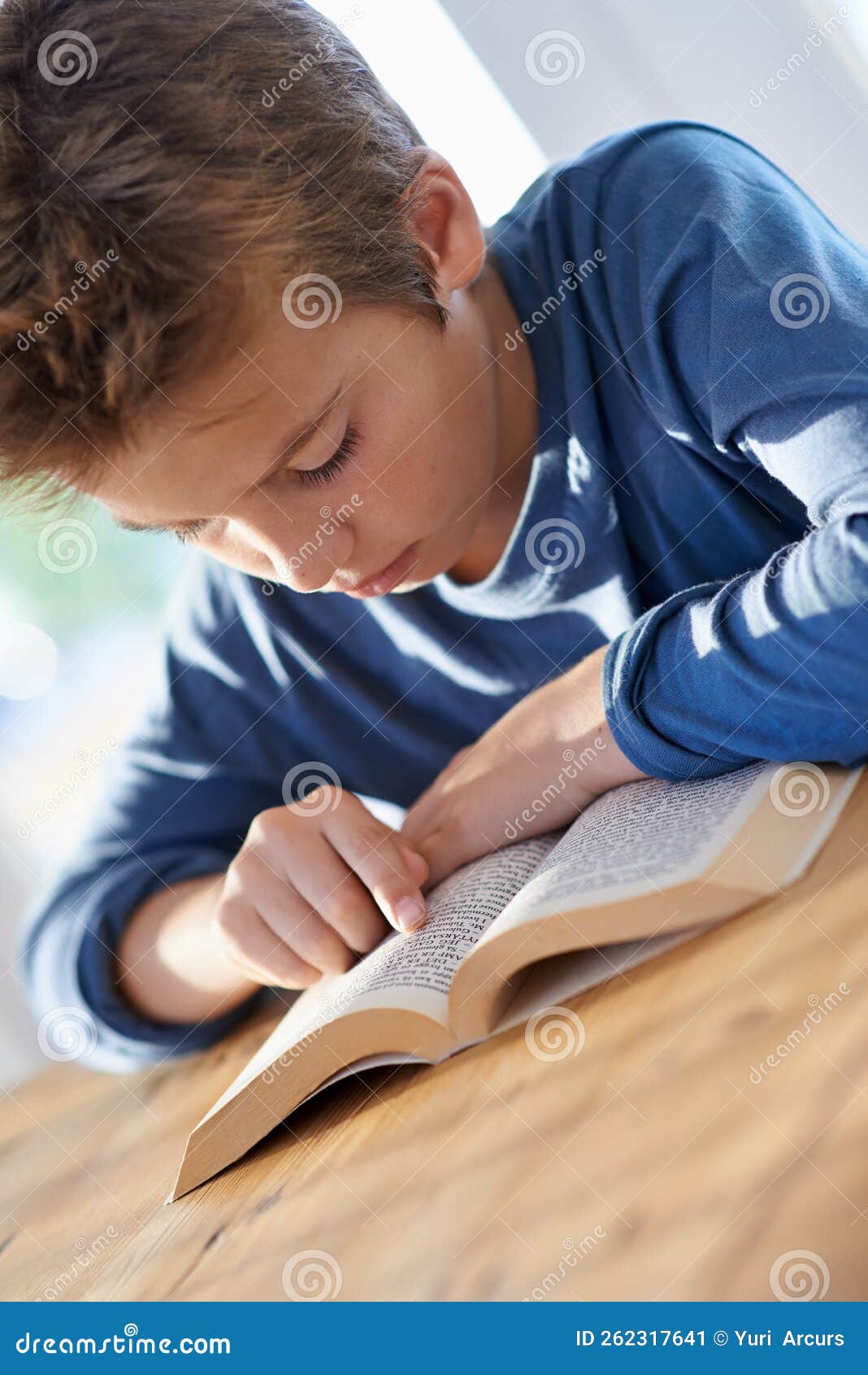 Hes really Getting into it. a Young Boy Reading a Book at a Table ...