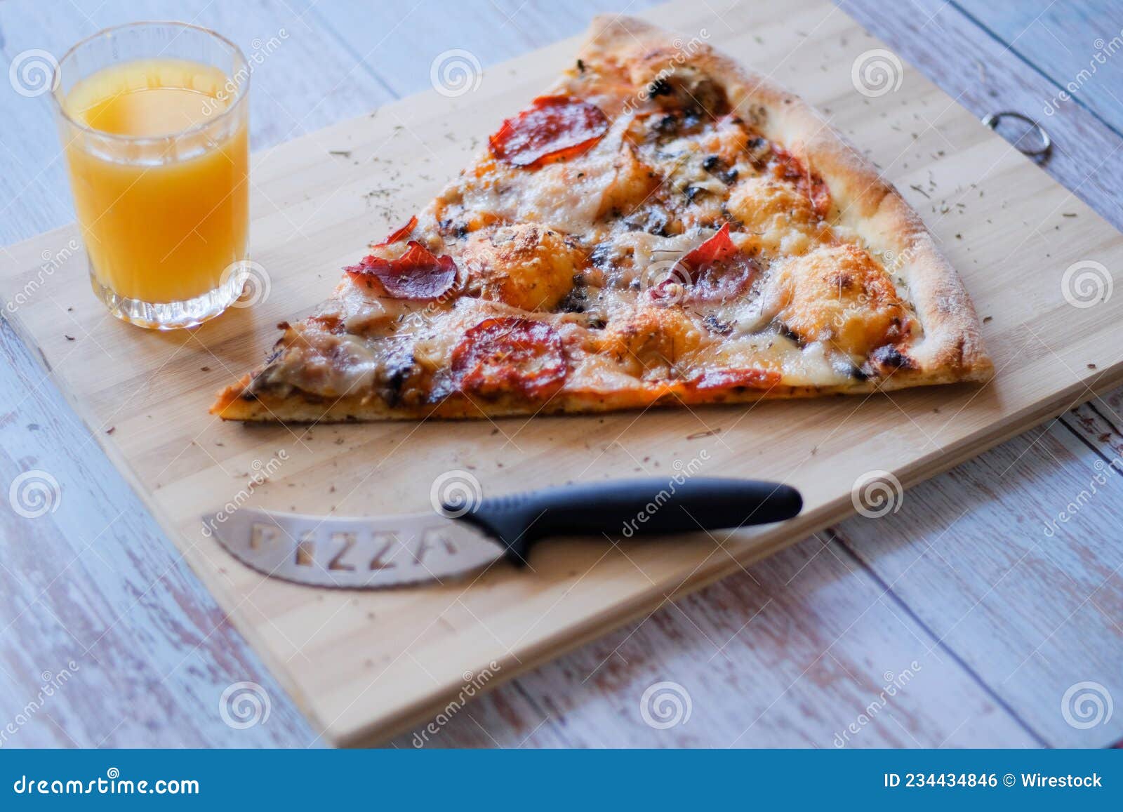 High Angle Shot of a Pizza Slice and an Orange Juice on a Cutting Board ...