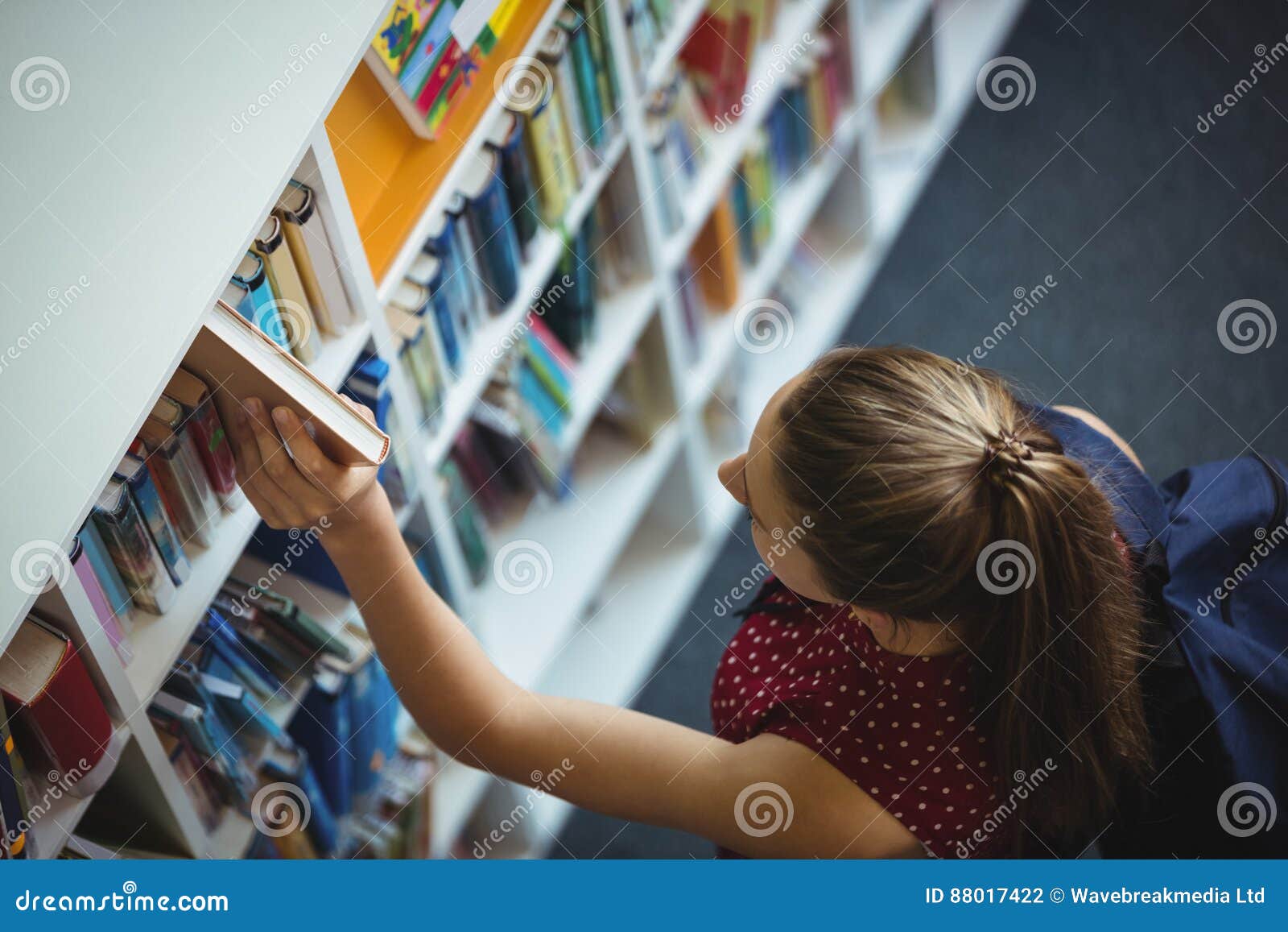 High Angle View of Schoolgirl Selecting Book from Bookshelf in Library ...
