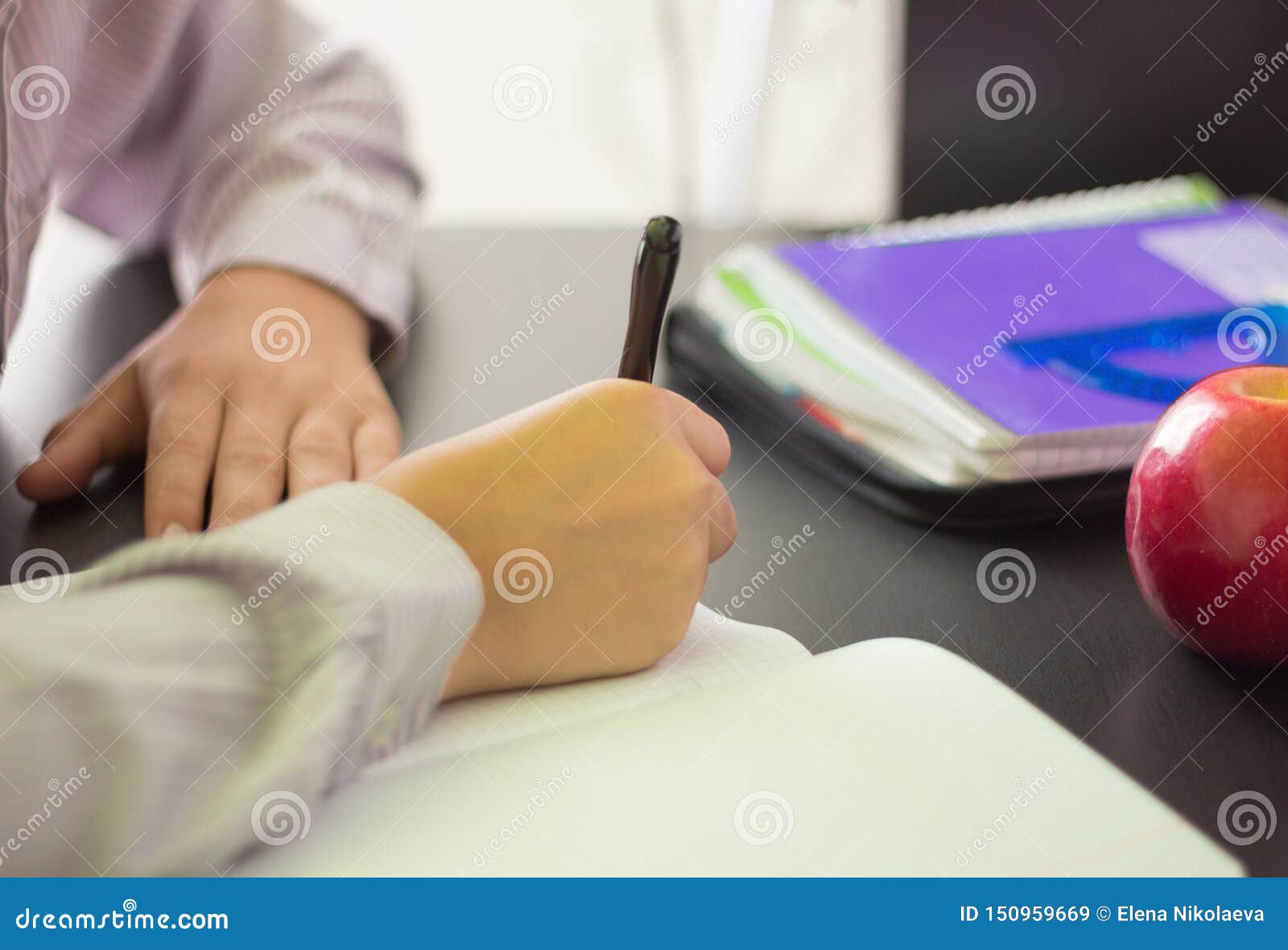 A High School Student or a Student Writes in a Notebook at a Desk ...