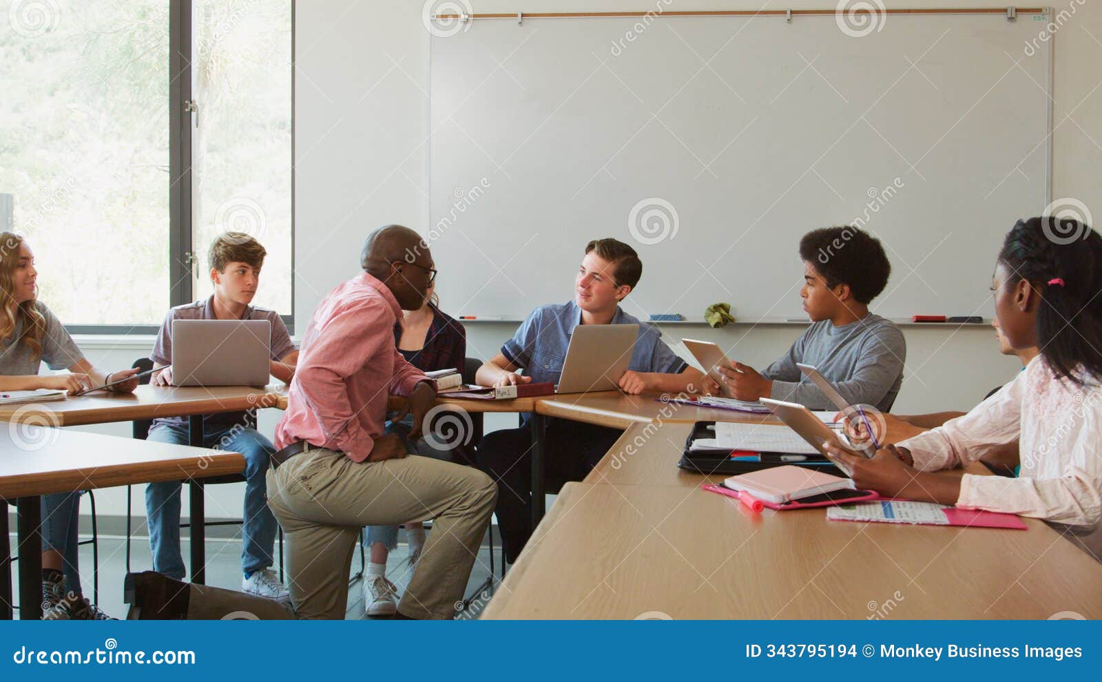 High School Teacher Helping Students Sitting at Desks Using Laptops and ...