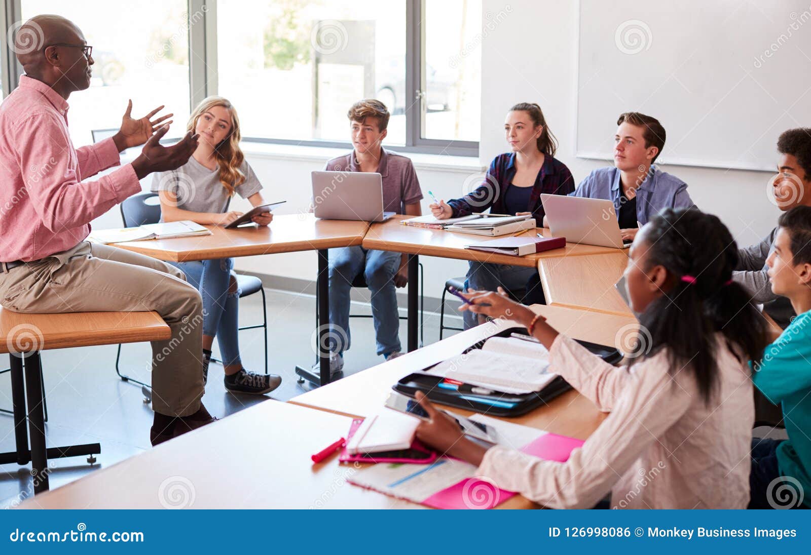 High School Teacher Talking To Pupils Using Digital Devices in ...