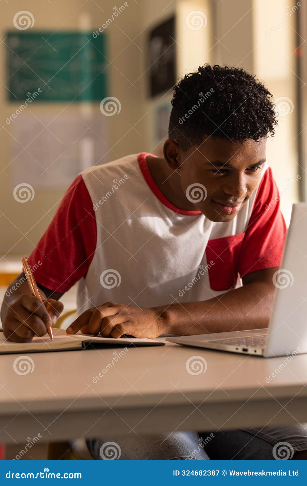 In High School, Teenage Boy Writing in Notebook while Using Laptop in ...