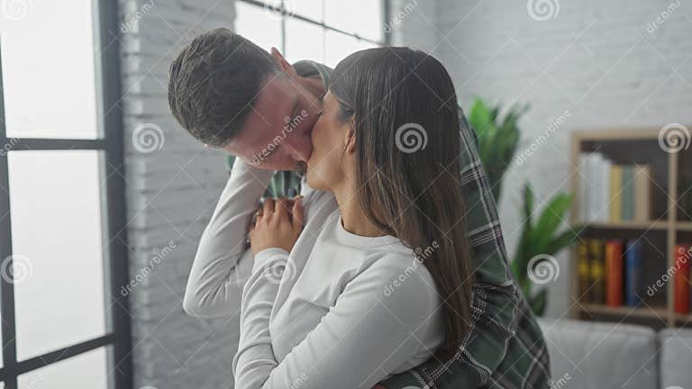 Hispanic Couple Affectionately Kissing Indoors In A Cozy Well Lit Living Room With A Modern