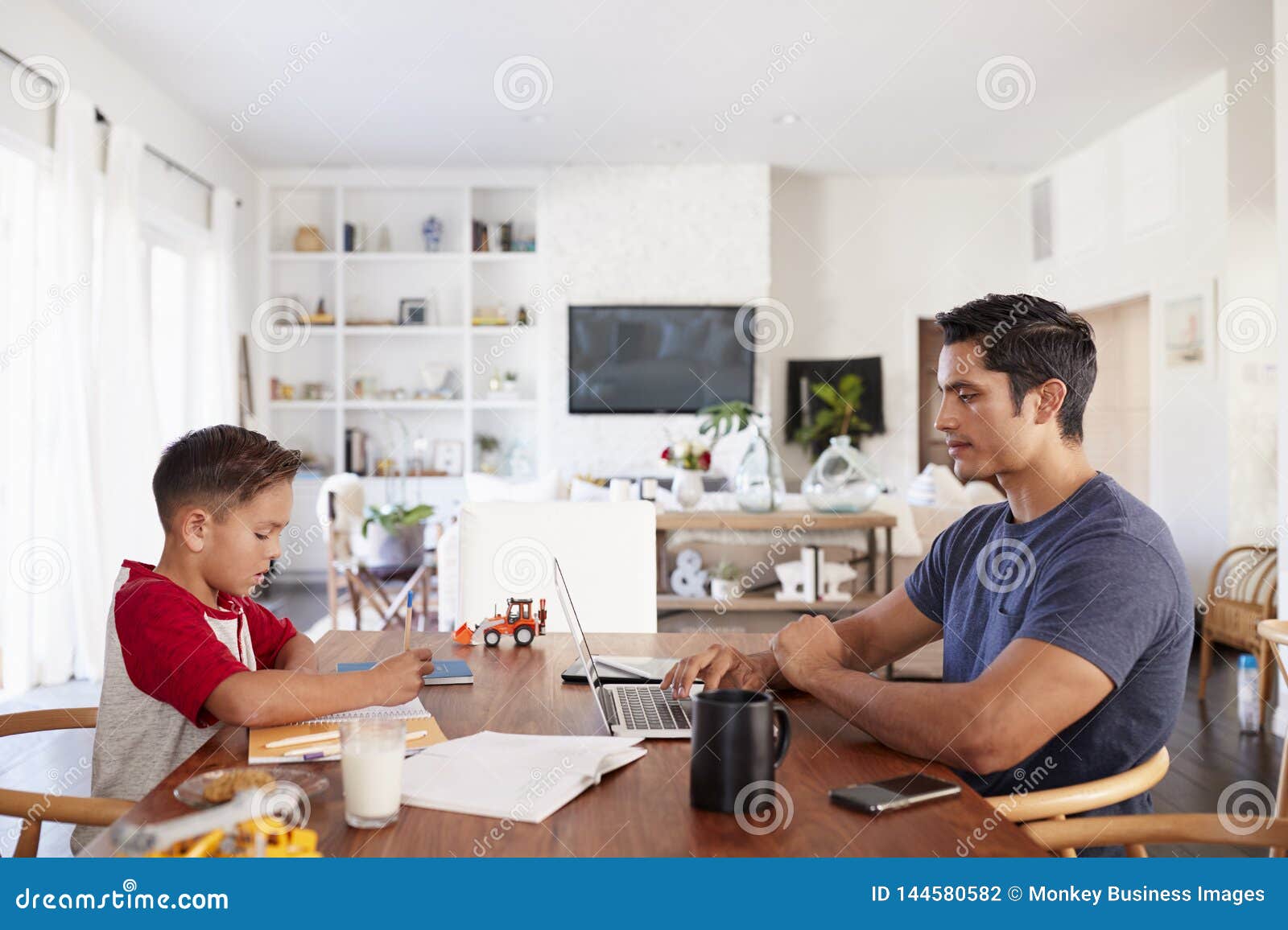 Hispanic Father and Son Working Opposite Each Other at the Dining Room ...
