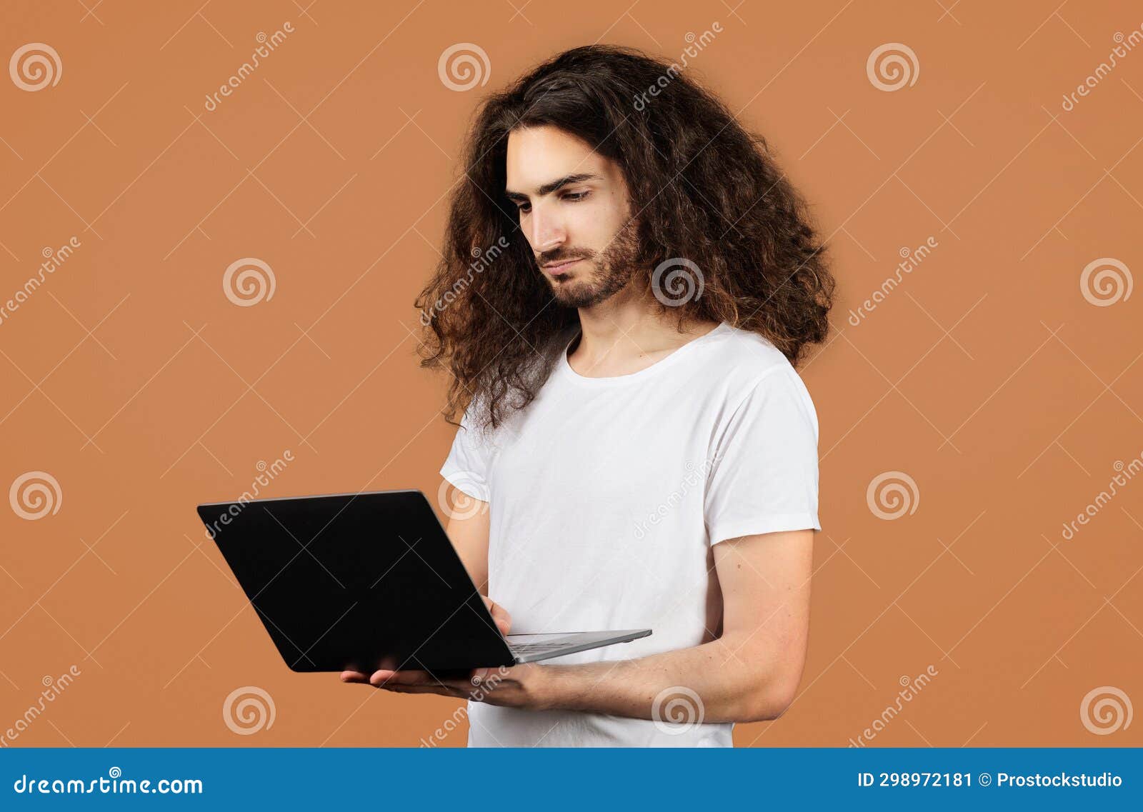 Hispanic Guy Seriously Works on His Laptop Computer, Beige Backdrop ...