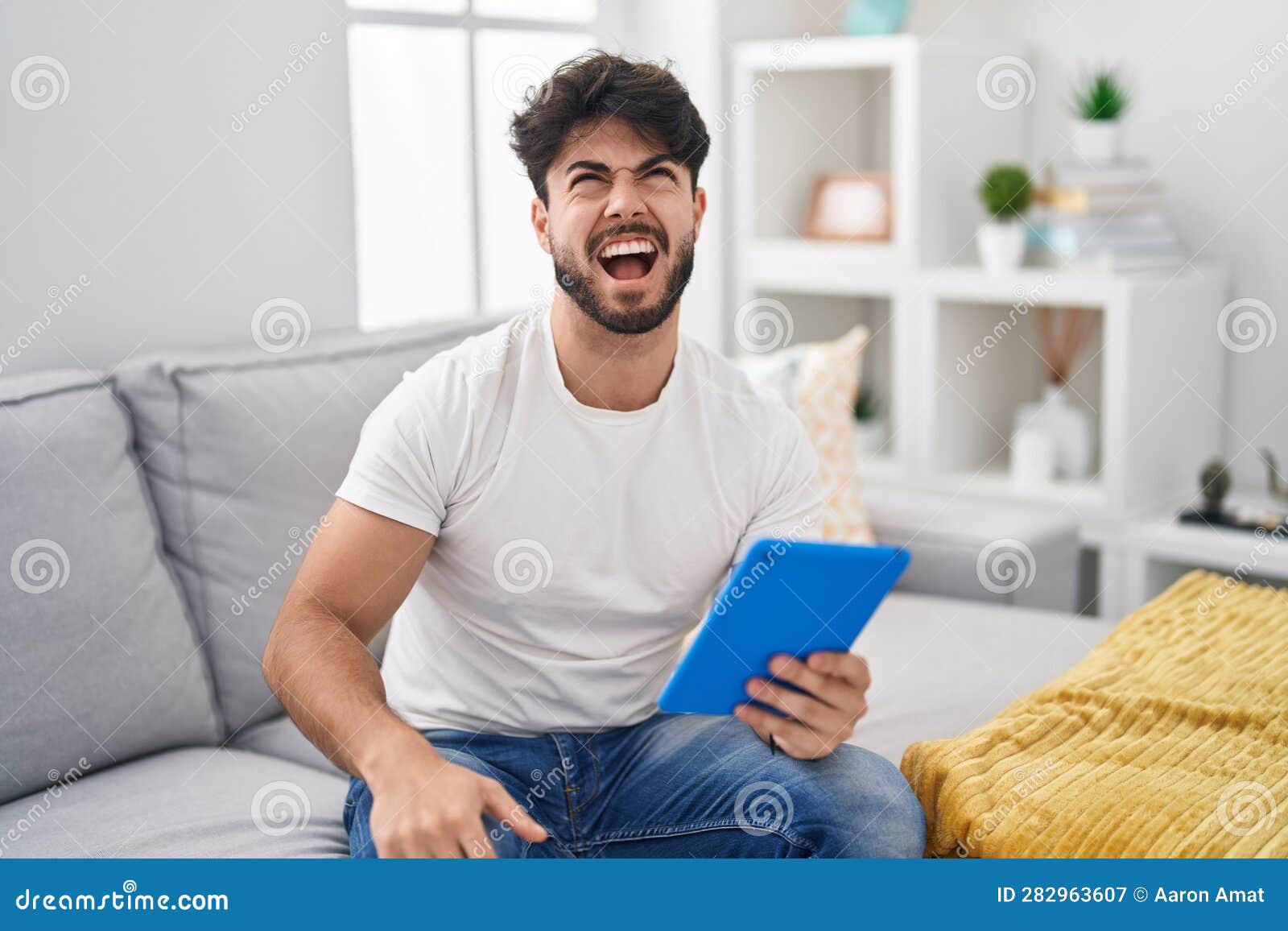 Hispanic Man with Beard Using Touchpad Sitting on the Sofa Angry and ...