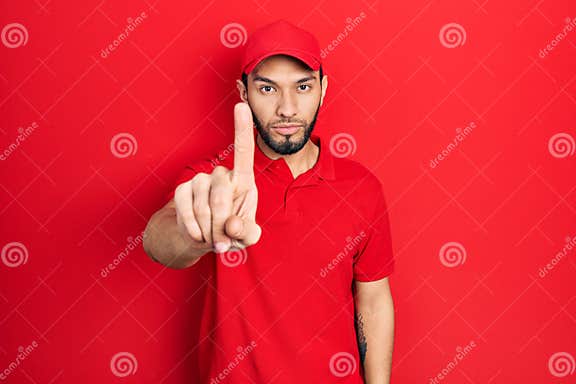 Hispanic Man With Beard Wearing Delivery Uniform And Cap Pointing With