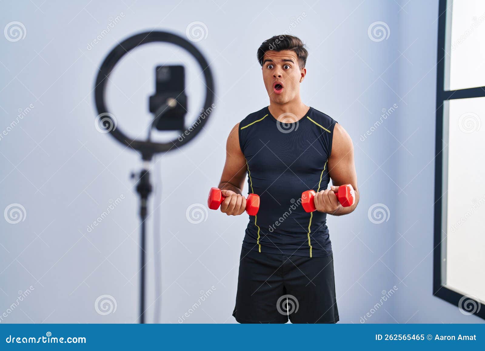 Hispanic Man Recording Training Tutorial at the Gym Afraid and Shocked ...