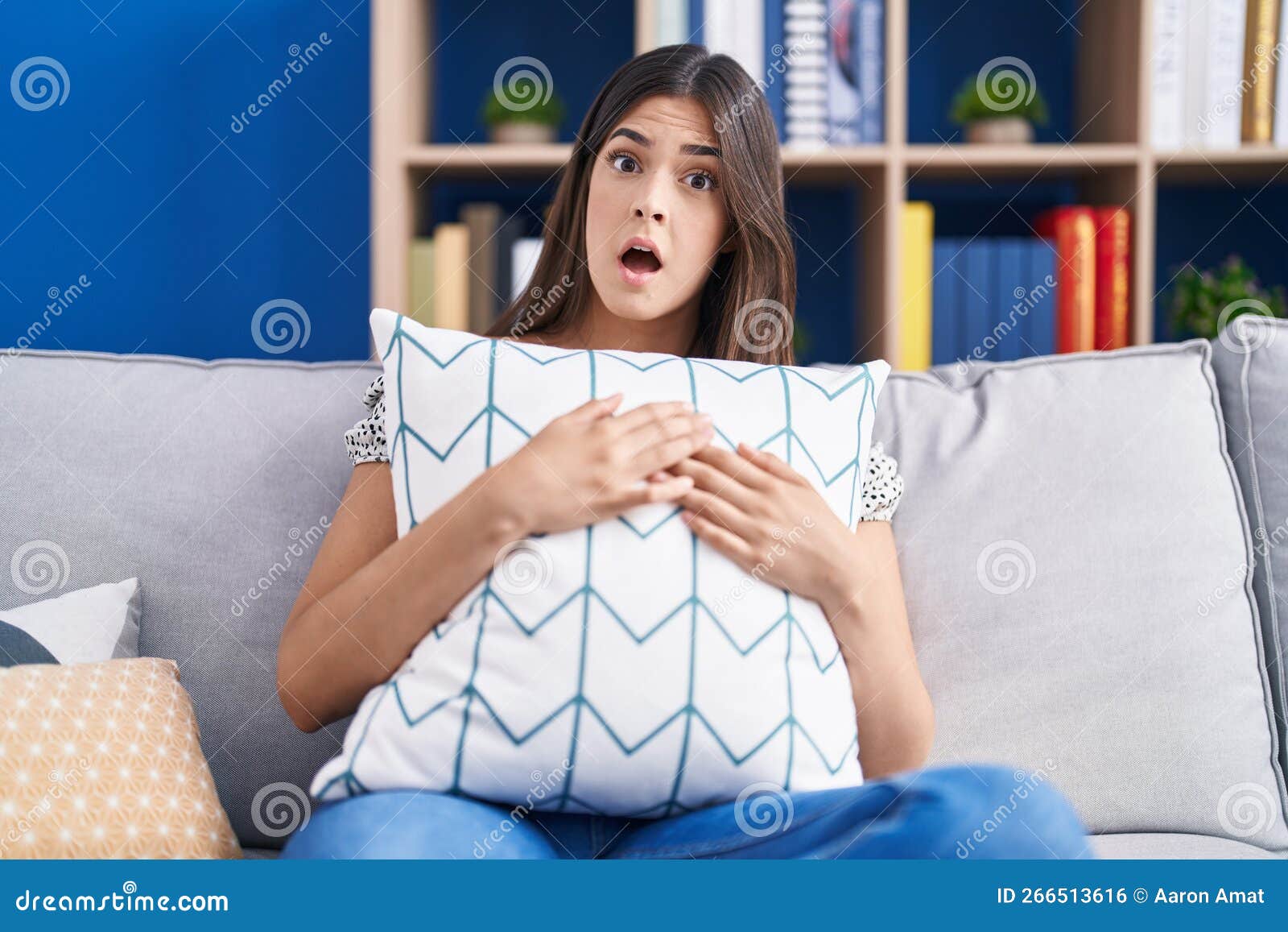 Hispanic Woman Hugging Pillow Sitting On The Sofa In Shock Face