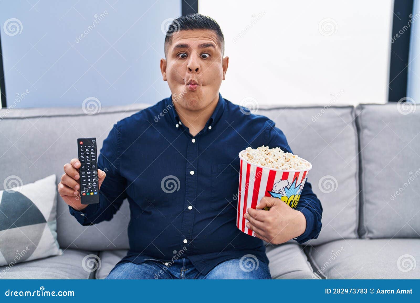 Hispanic Young Man Eating Popcorn Using Tv Control Making Fish Face ...