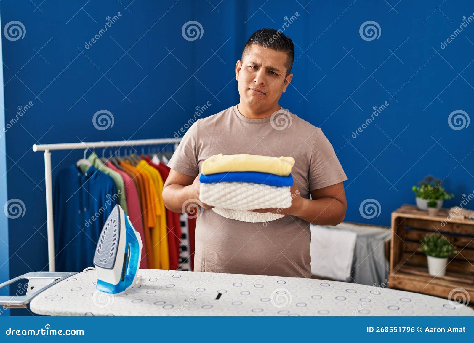 Hispanic Young Man Holding Folded Laundry after Ironing Depressed and ...
