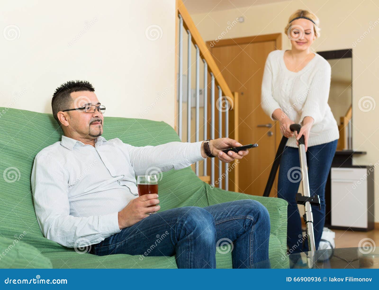 Hombre Que Ve La Tv Mientras Que La Mujer Limpia Foto De Archivo