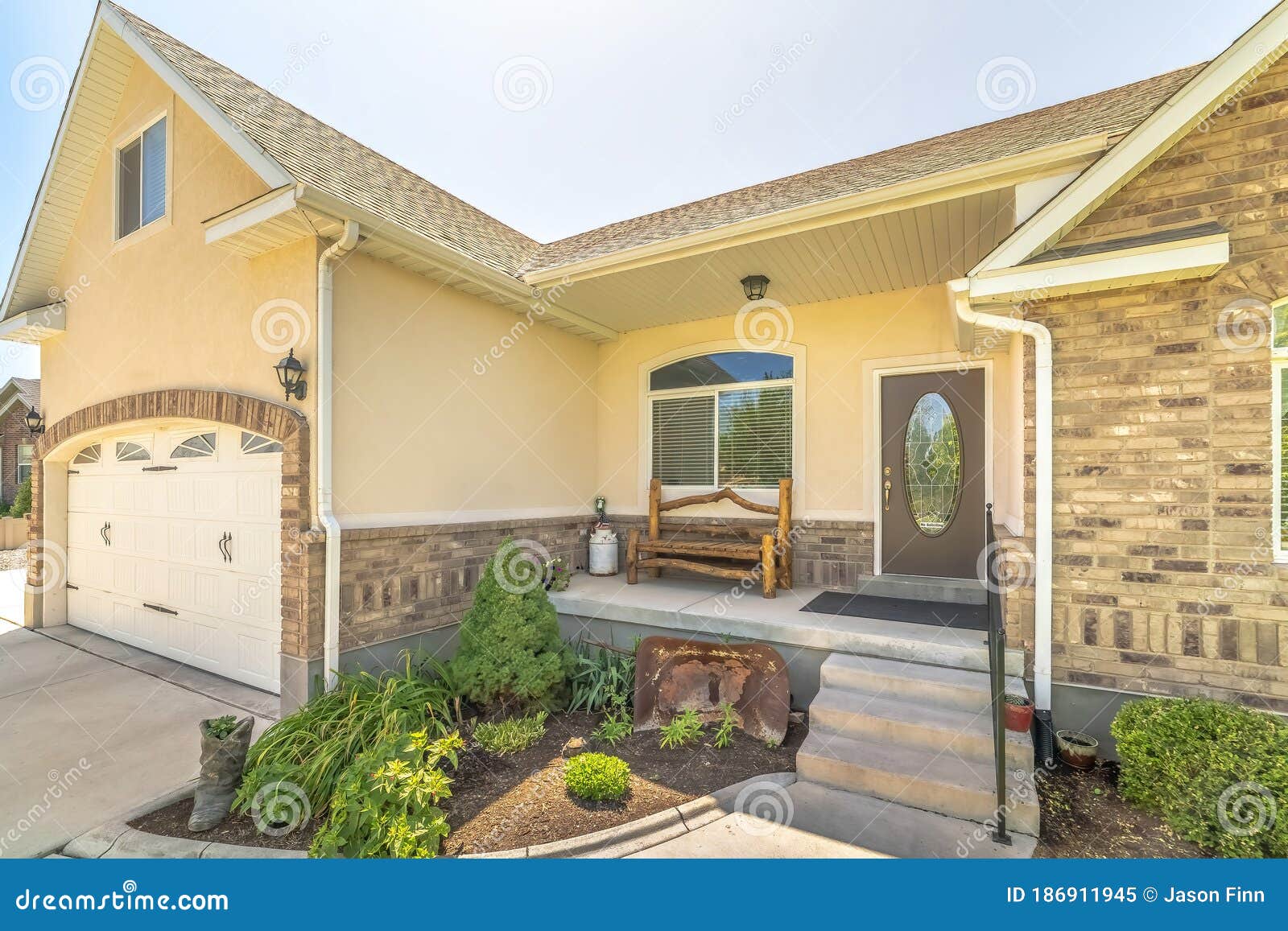 Home Facade With View Of Arched Garage Door And Front Door With Oval Glass Pane Stock Image