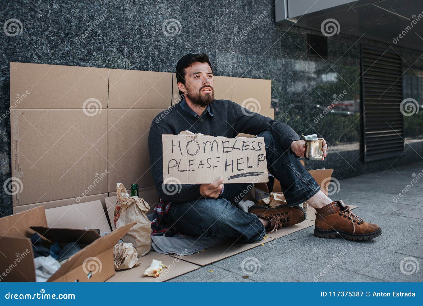 Homeless Man Is Sitting On Cardboard And And Holding A Sign That Says