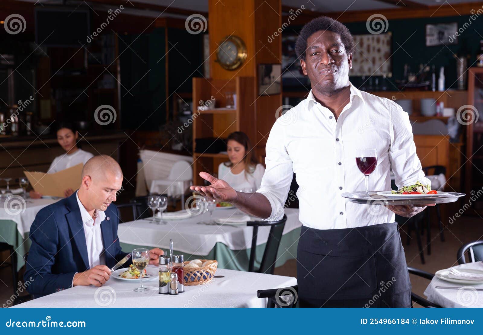 Hospitable African American Waiter Greeting Guests In Restaurant Stock