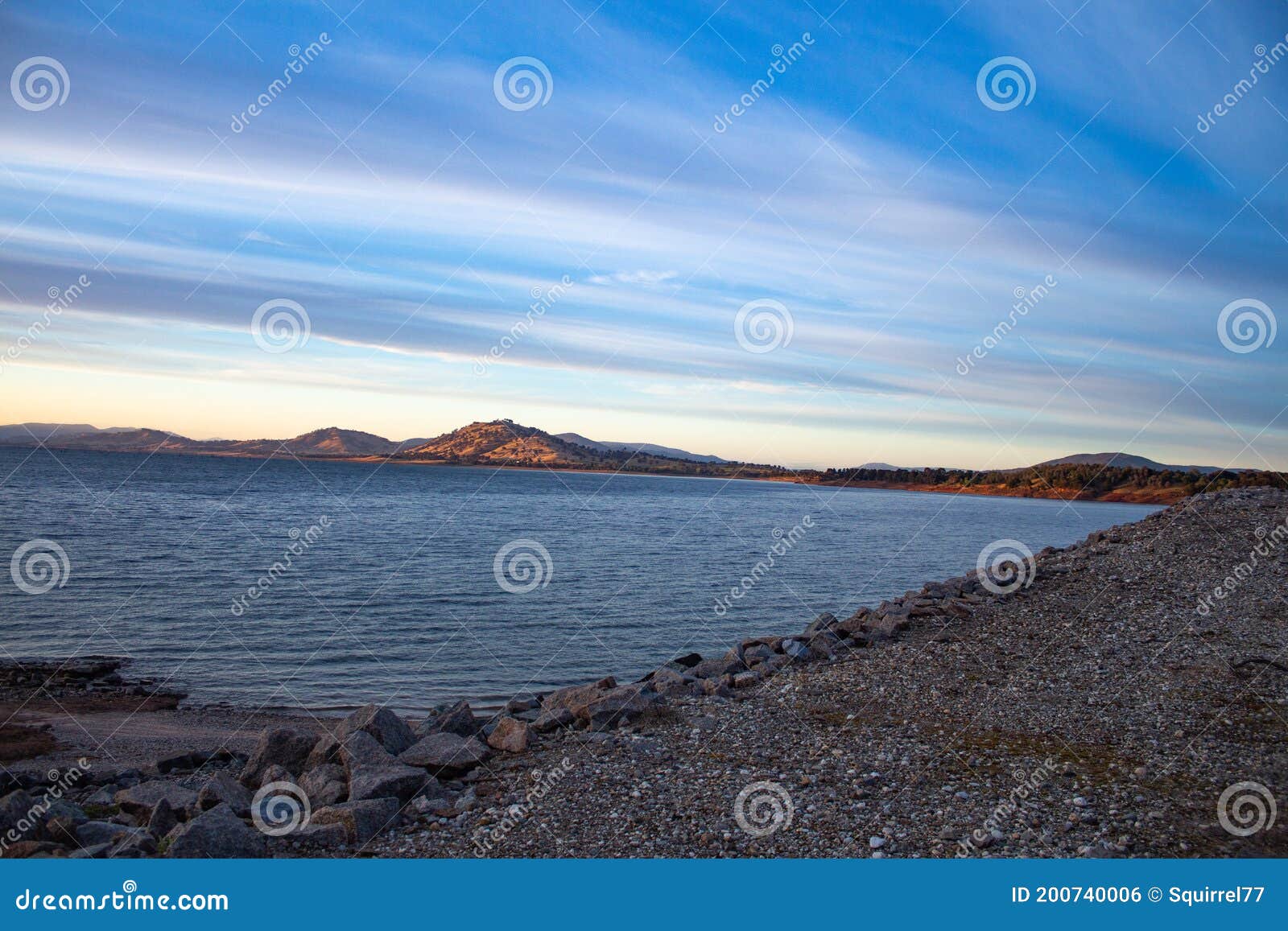 Blue Water Filled Lake Dam with Rocky Foreshore and Small Hills in ...