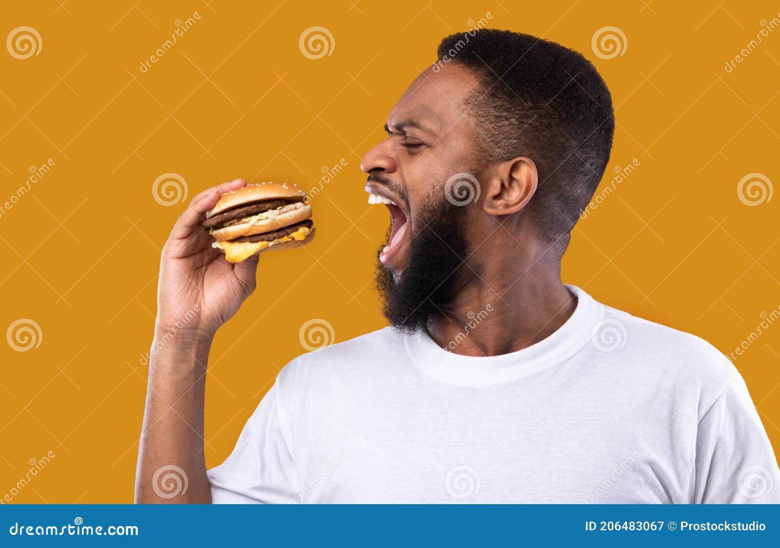 Hungry African Guy Biting Burger Posing on Yellow Background, Side-View ...