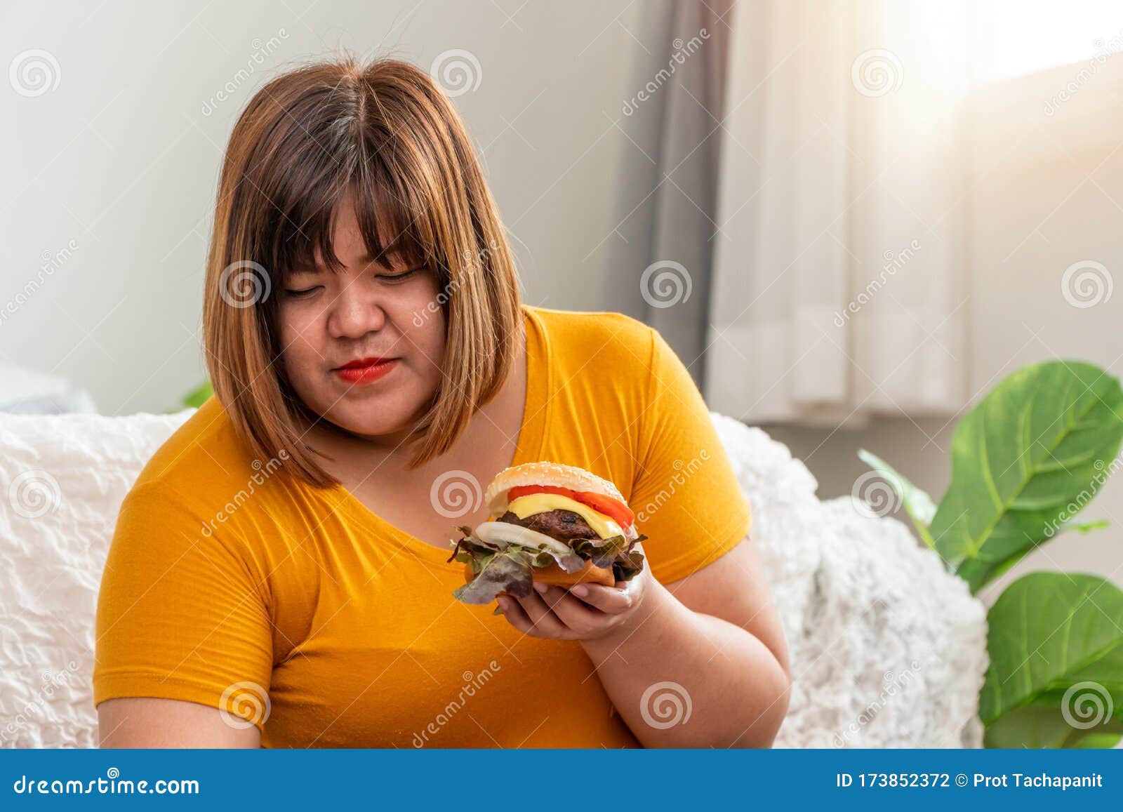 Hungry Overweight Woman Smiling And Holding Hamburger And Sitting In