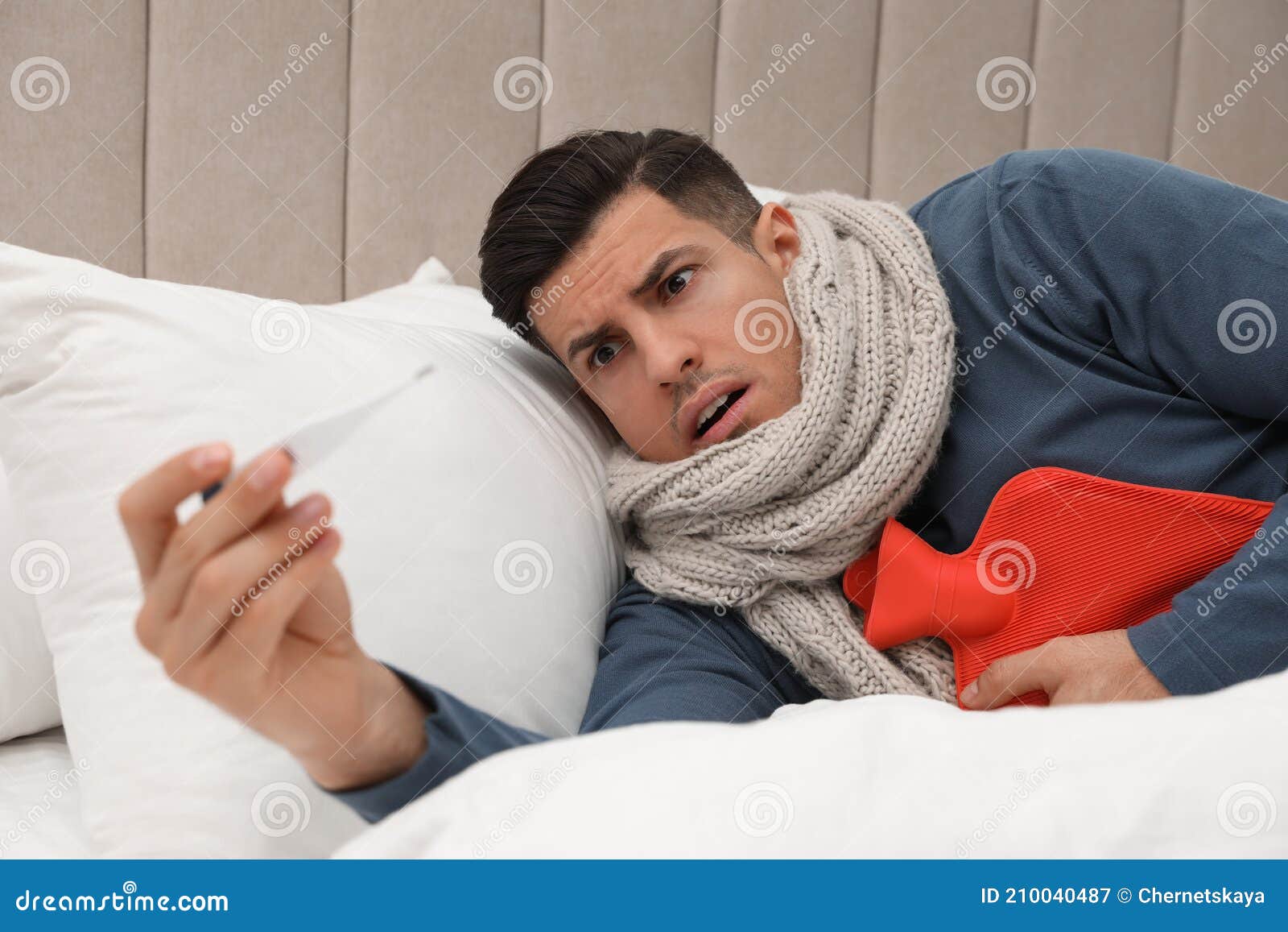 Ill Man with Hot Water Bottle Checking His Temperature at Home Stock ...