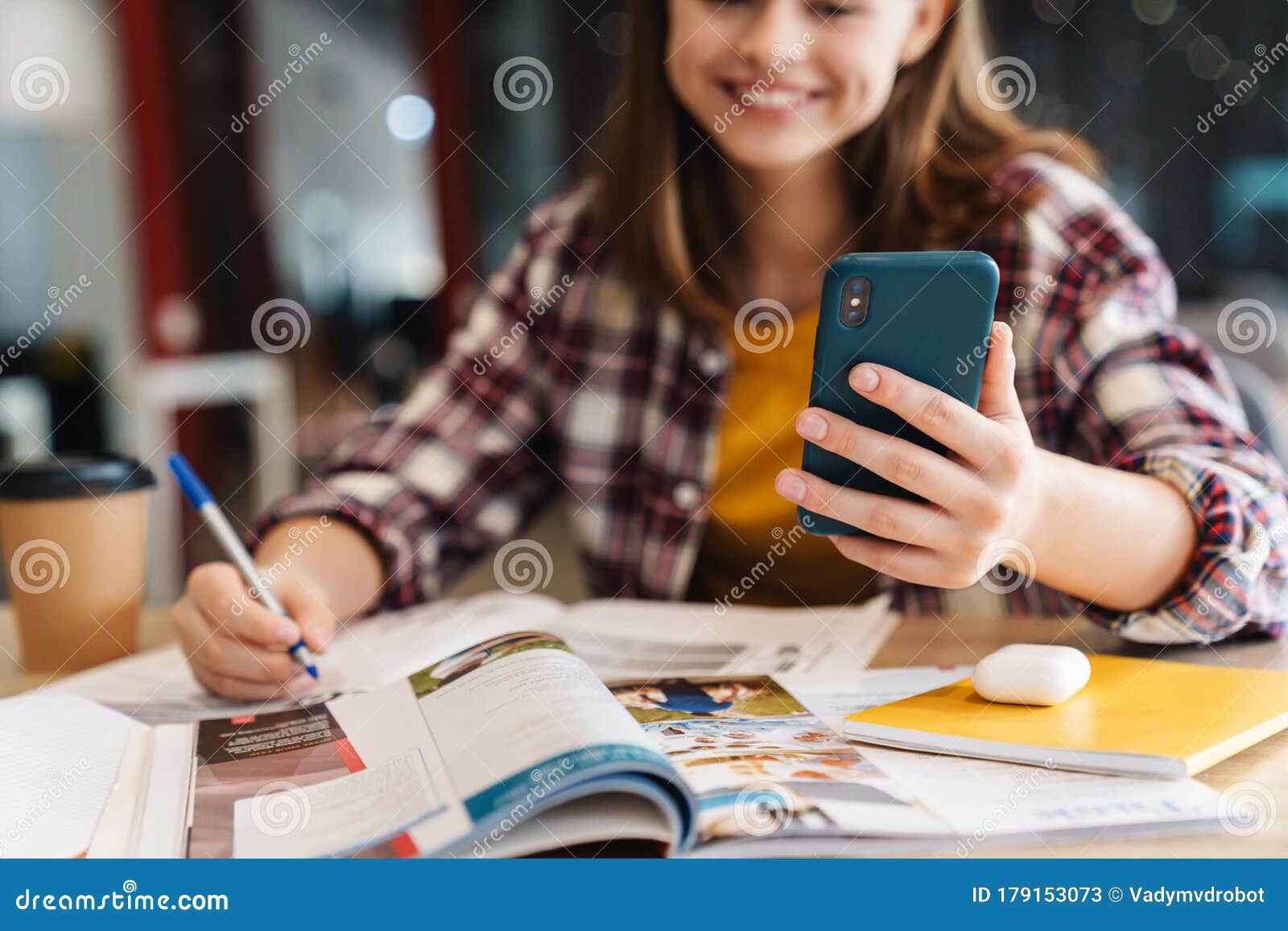 Image of Joyful Beautiful Girl Using Cellphone while Doing Homework ...