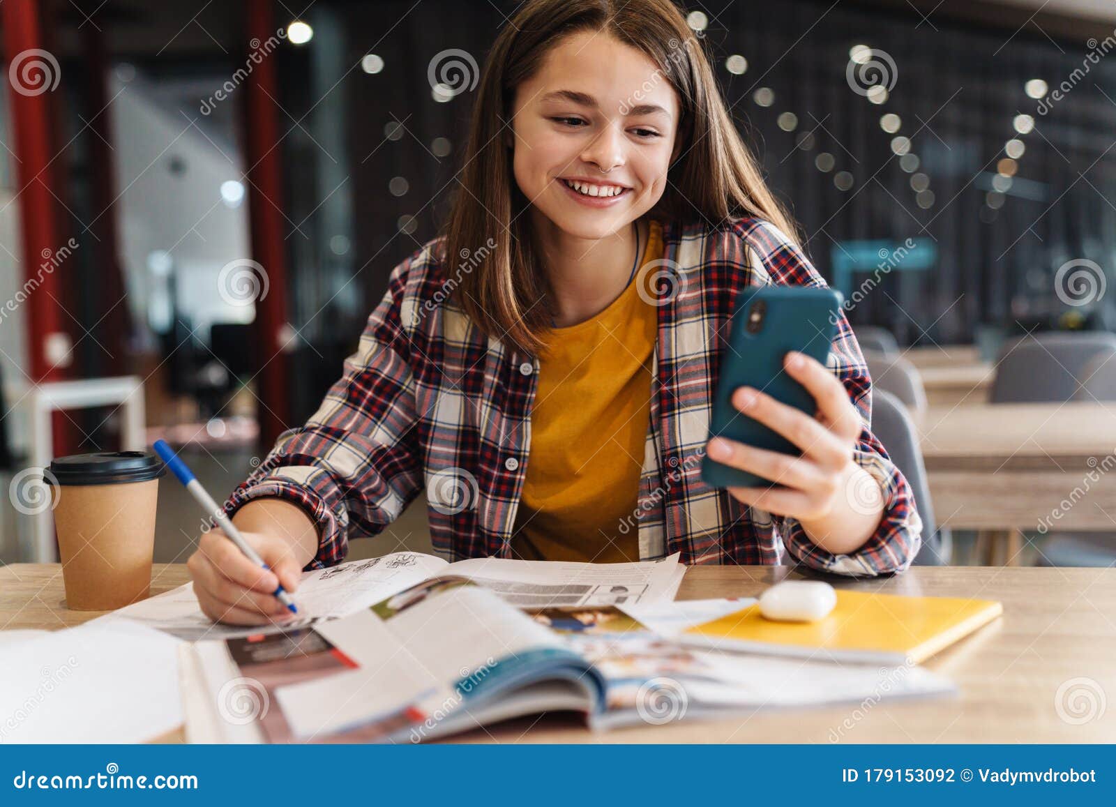 Image of Joyful Beautiful Girl Using Cellphone while Doing Homework ...