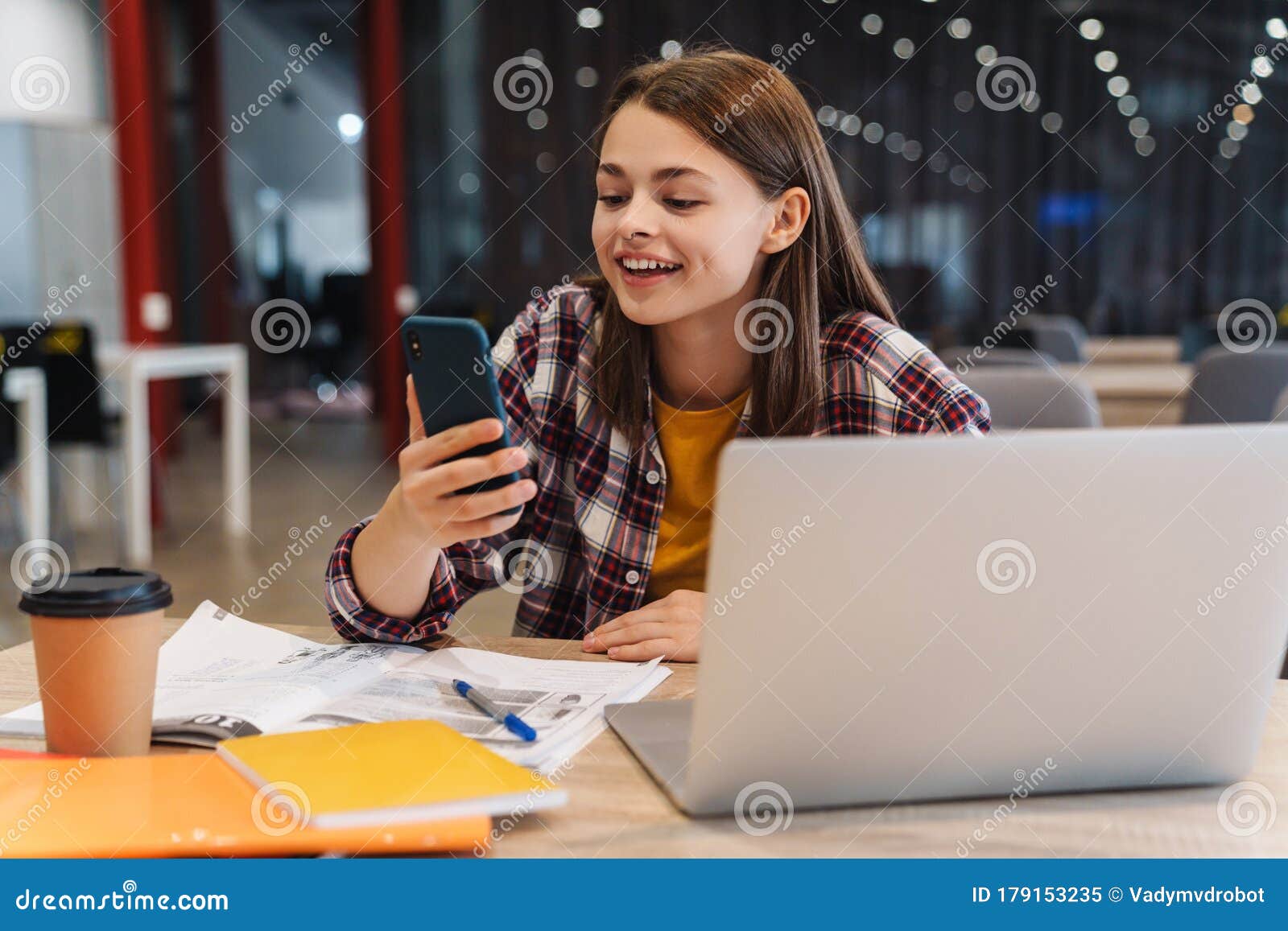 Image of Smiling Girl Using Cellphone while Doing Homework with Laptop ...