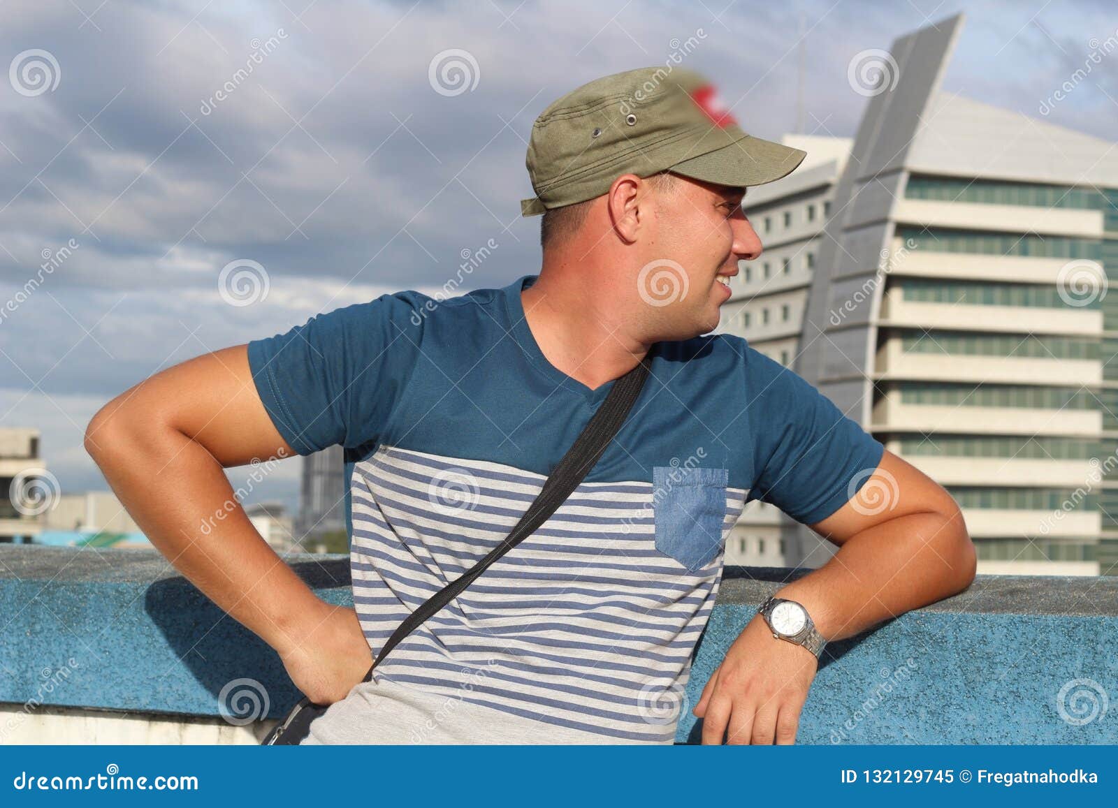 A Young Man in a Cap in Profile Against the Background of Buildings ...