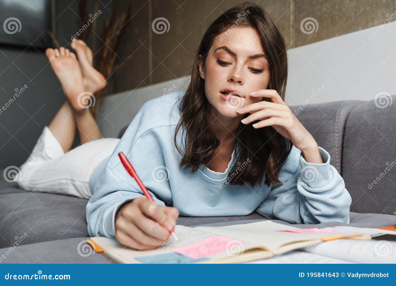 Image of Woman Doing Homework with Exercise Books while Lying on Sofa ...